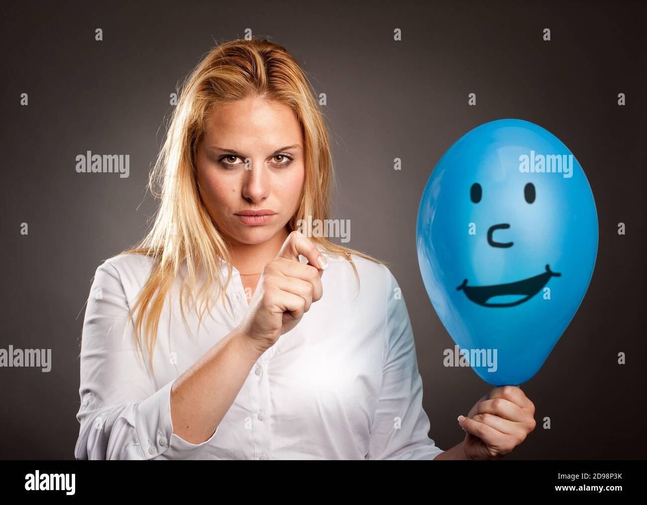young woman piercing a balloon with a needle on gray background Stock ...