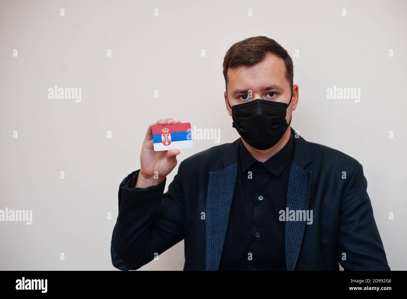 European Man Wear Black Formal And Protect Face Mask Hold Serbia Flag Card Isolated On White