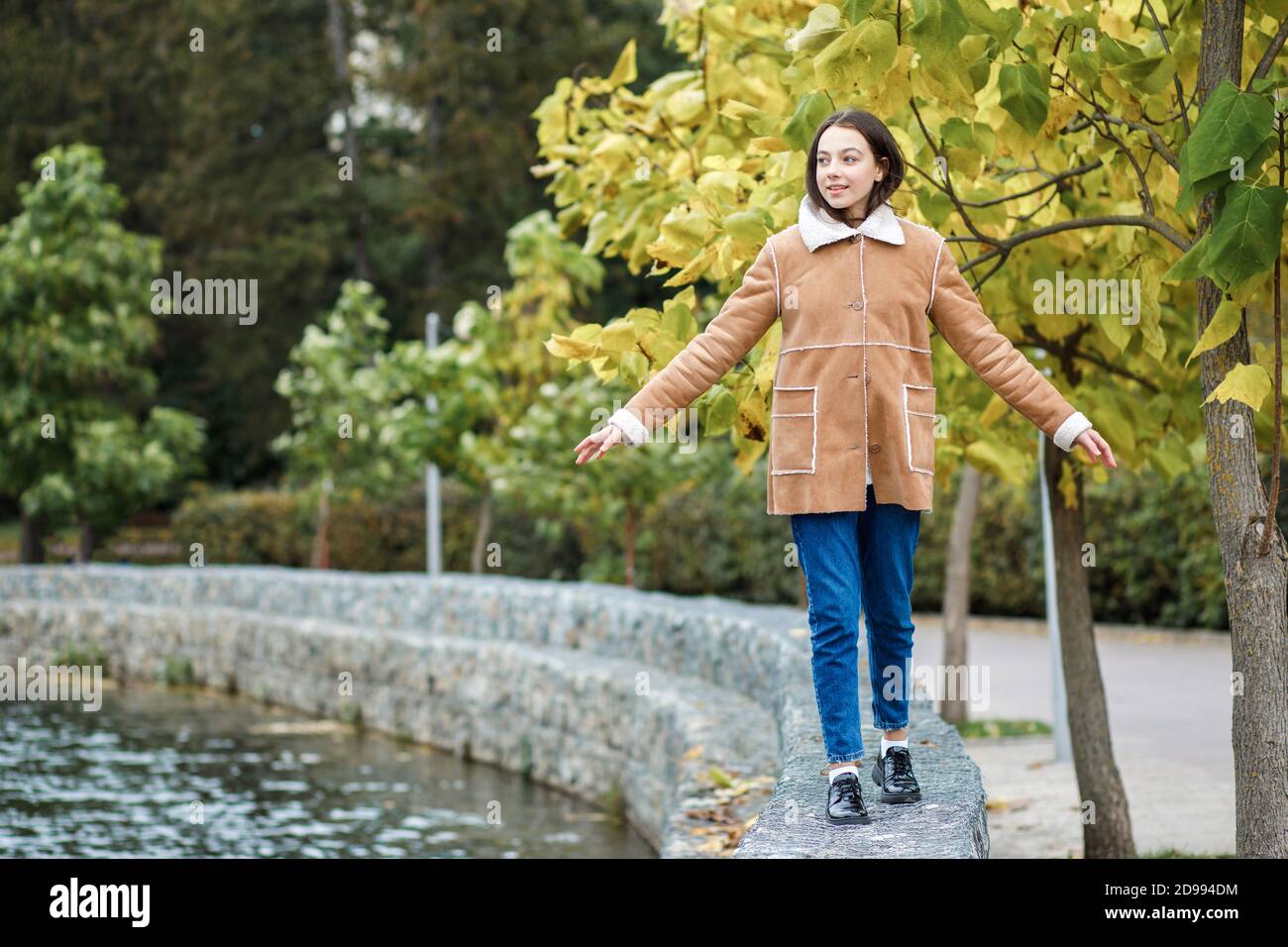 Young pretty teenage girl in warm clothes walks in the park in autumn ...