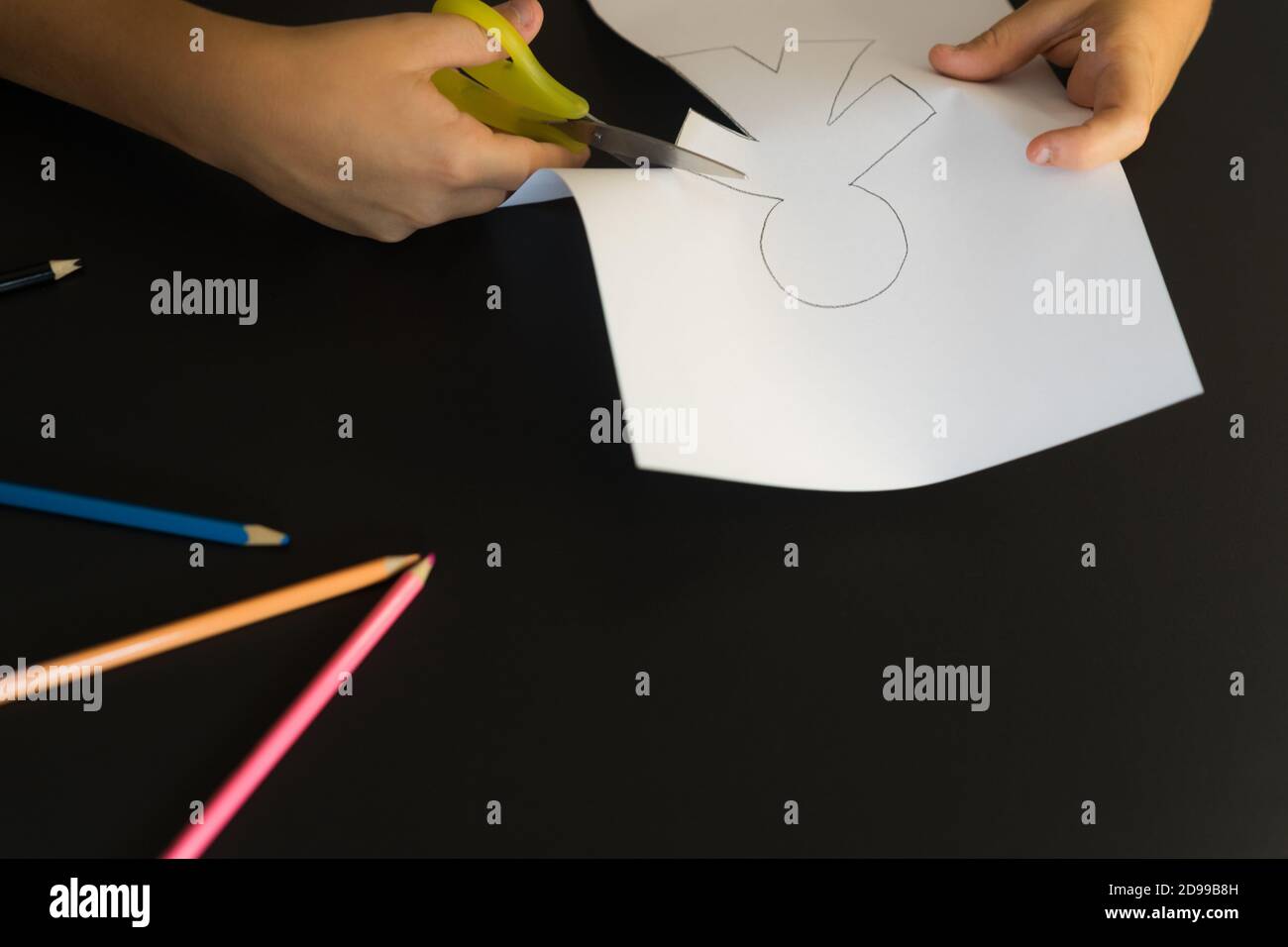 Closeup shot of a child hand cutting the sketch of a human on a paper ...