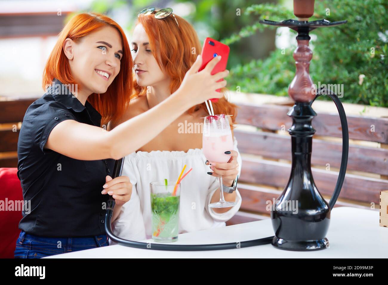 Two women smoke a hookah and enjoy cocktails in a cafe on the street ...