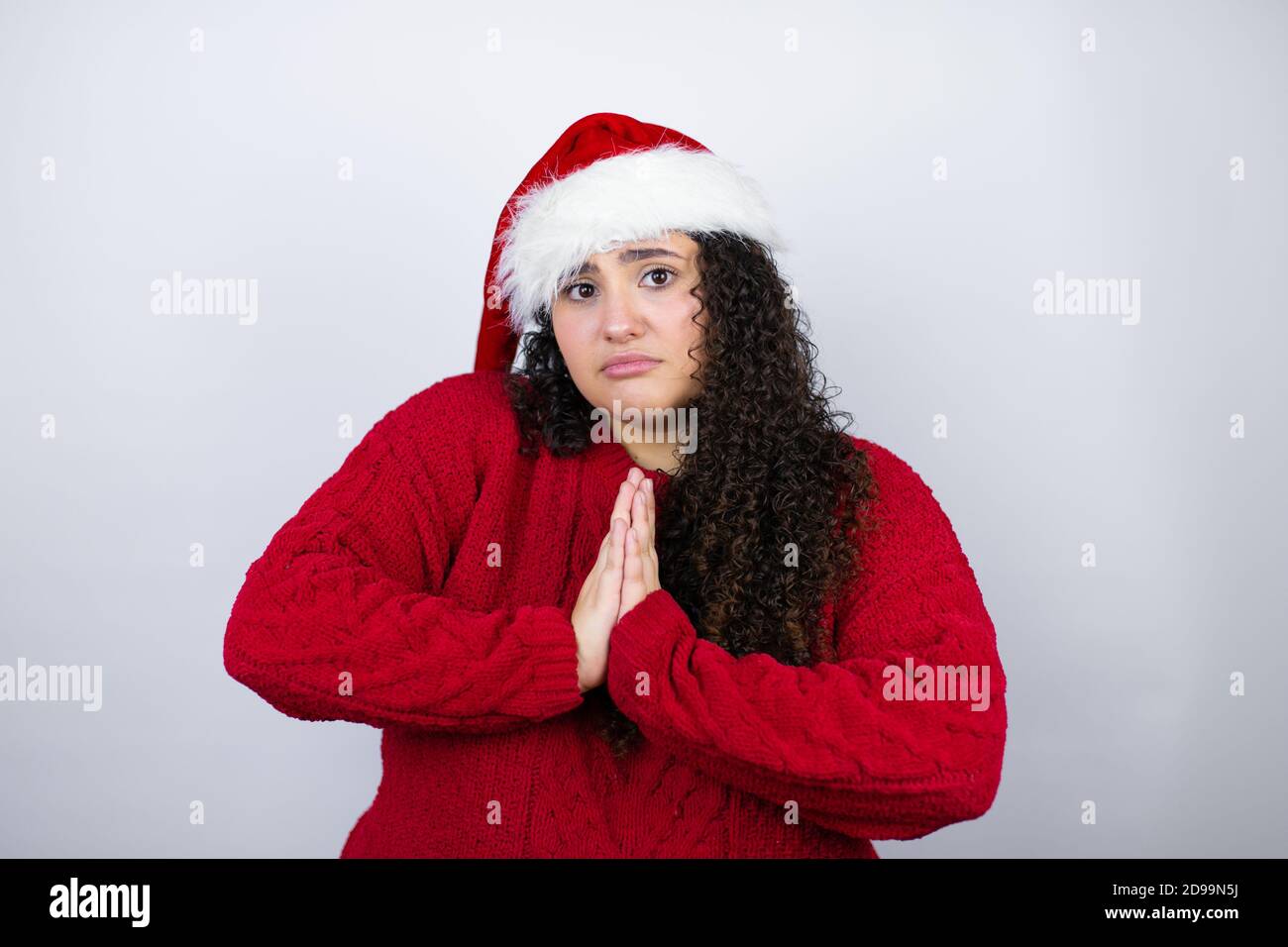 Young beautiful woman wearing a Santa hat over white background begging ...