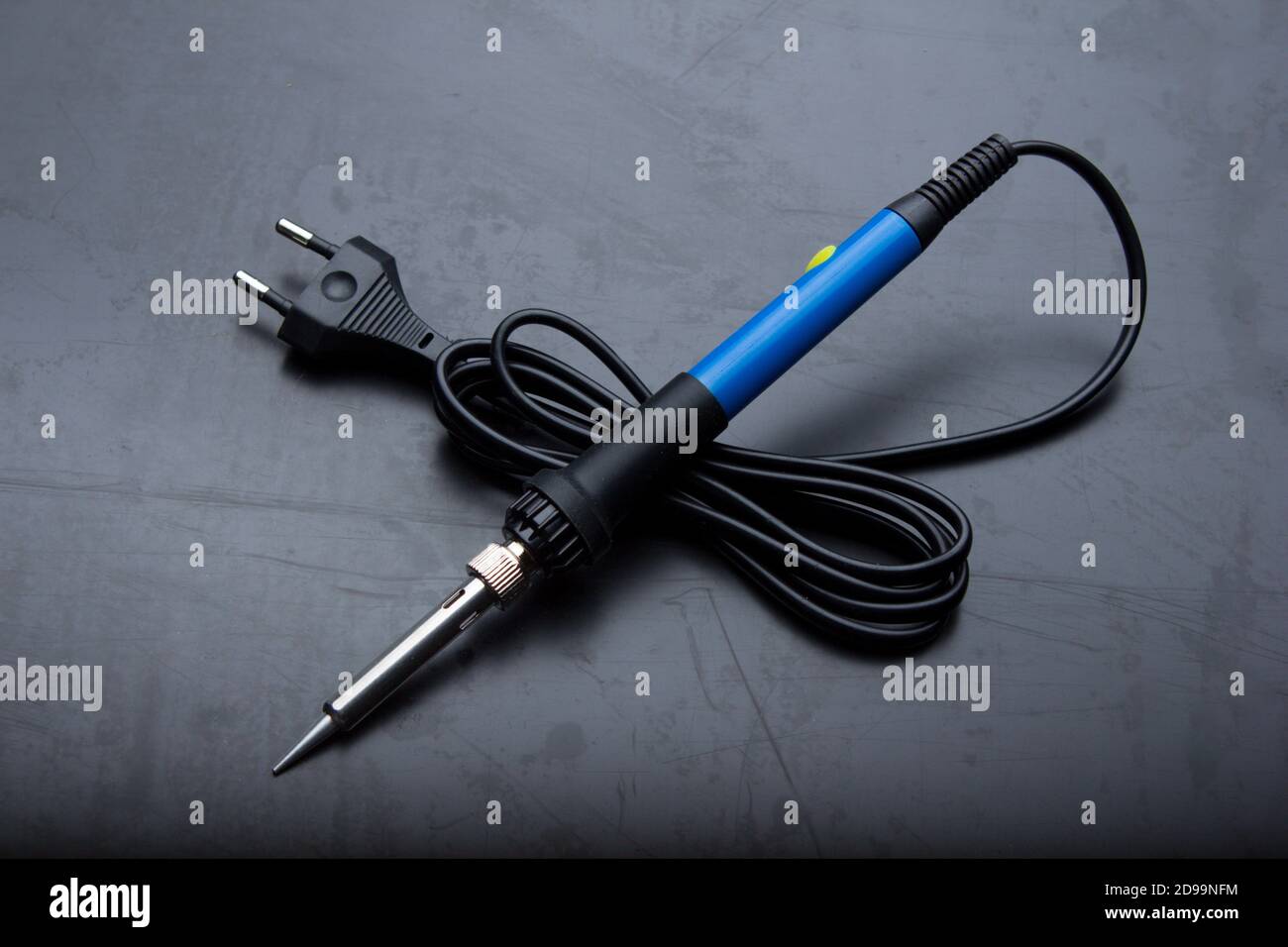 Soldering iron with a blue handle on the old black desktop surface ...