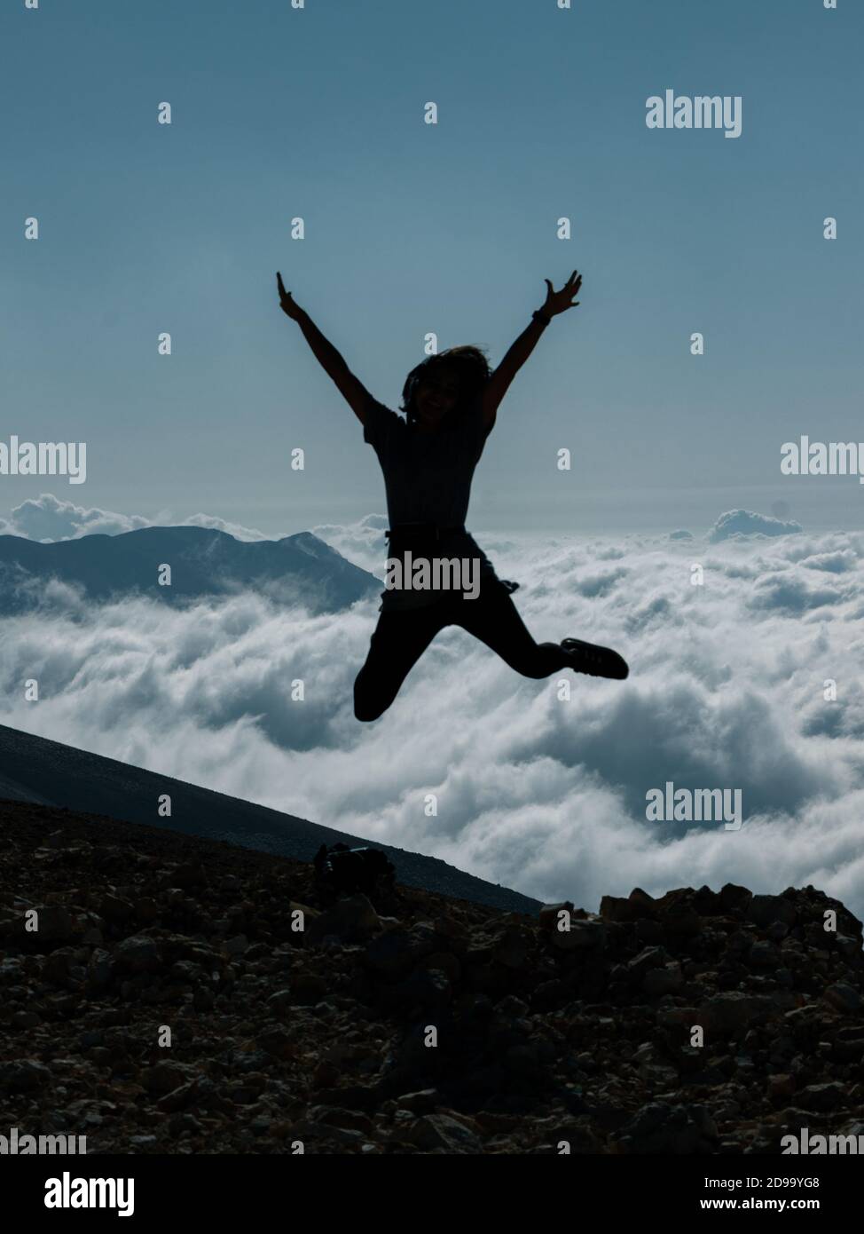 joyful jump silhouette above clouds with a a mountain peak behind her ...