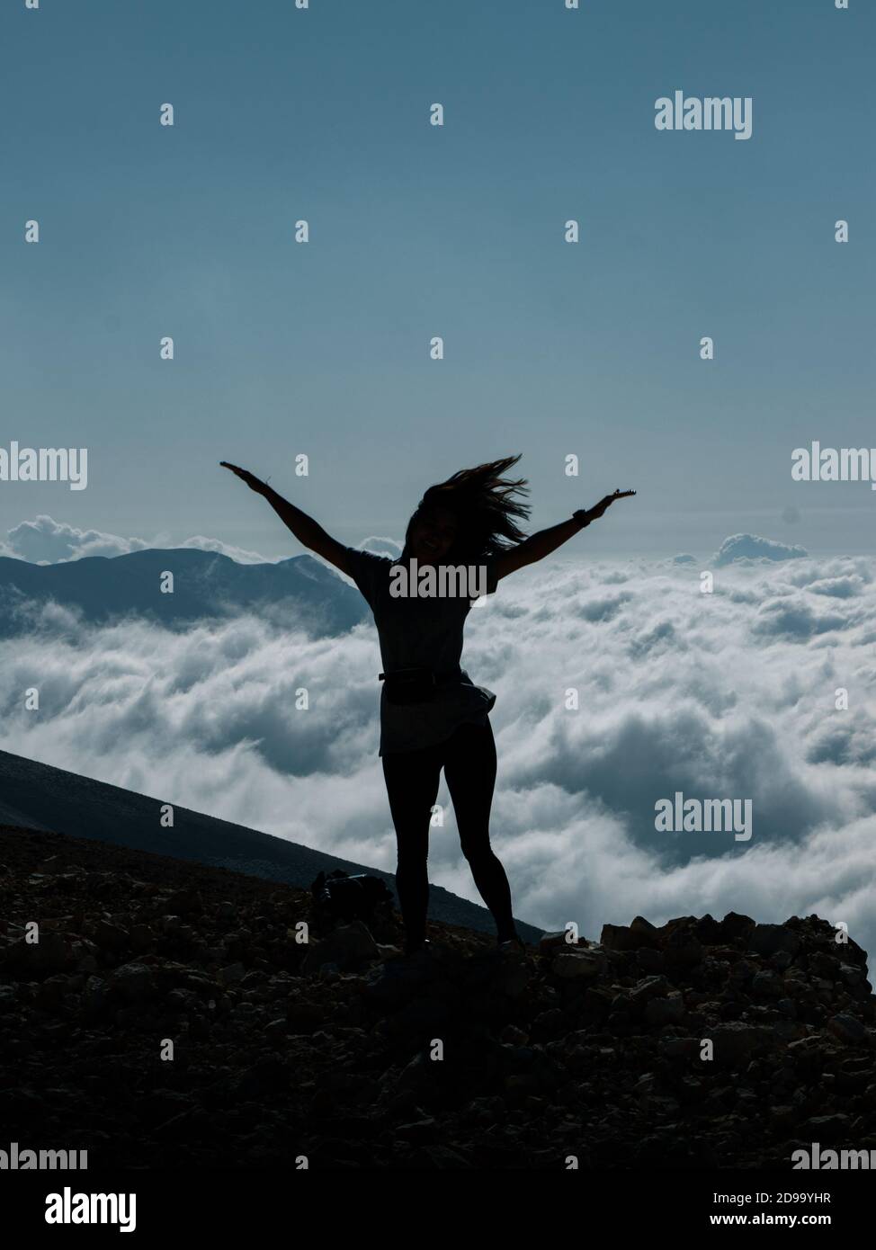 joyful jump silhouette above clouds with a a mountain peak behind her ...