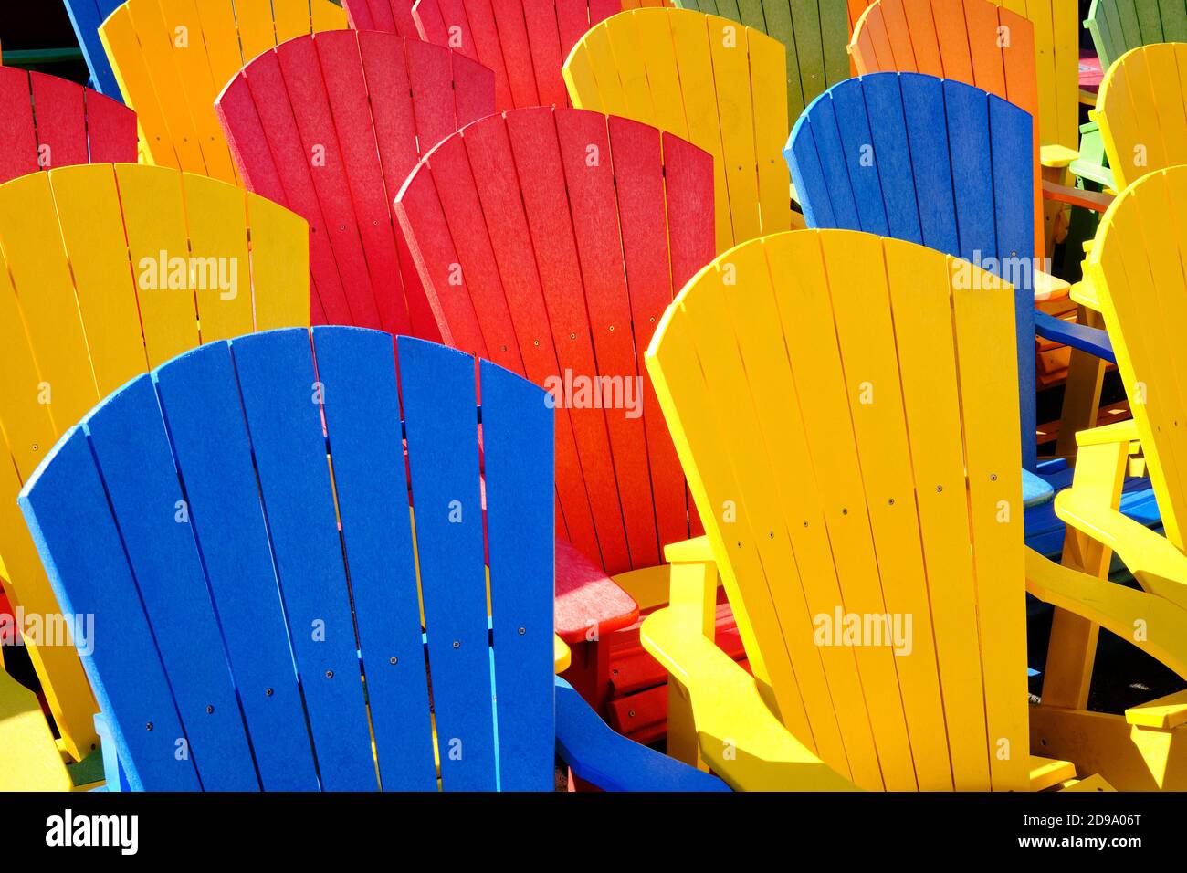 Back of Many multicolored Adirondack chairs with no one sitting set up ...