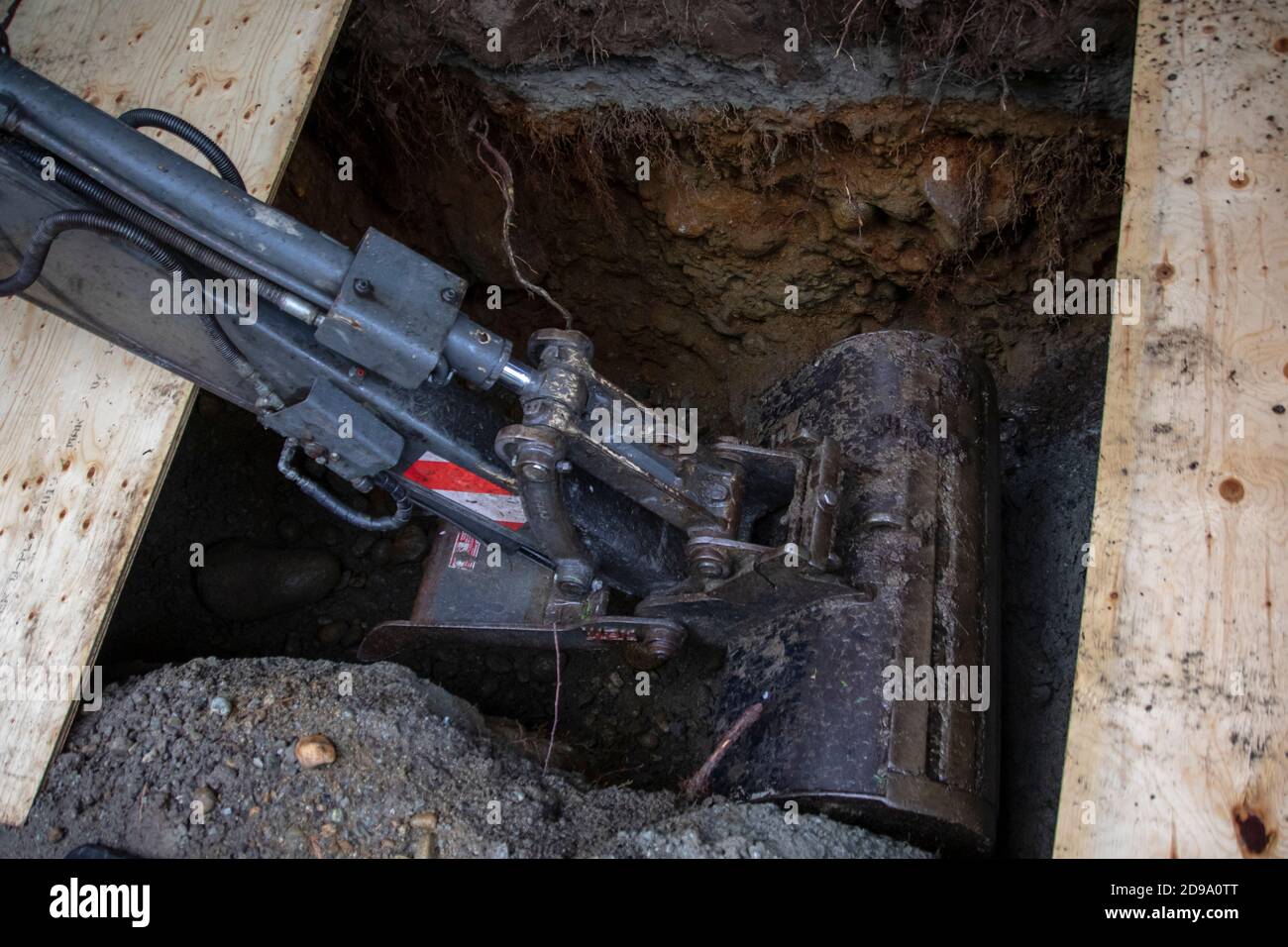 A backhoe in a trench with plywood covering the openings on either side ...