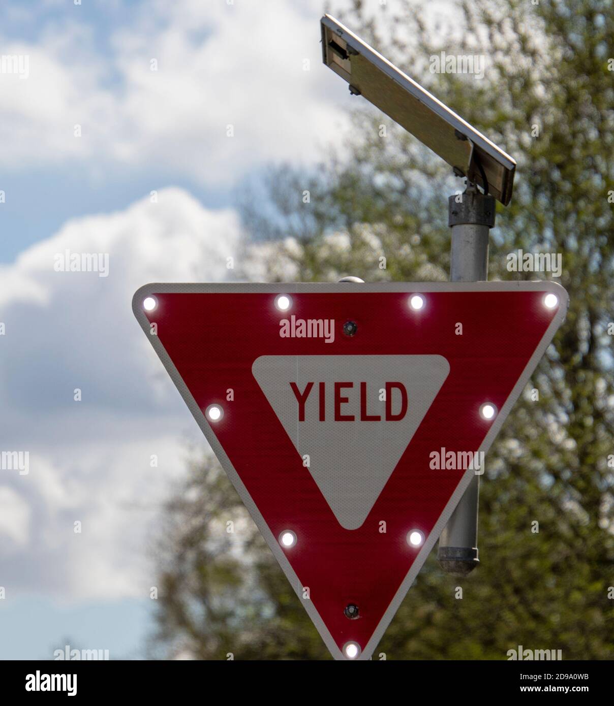 A yield sign with led lights on the edges with clouds on the left ...