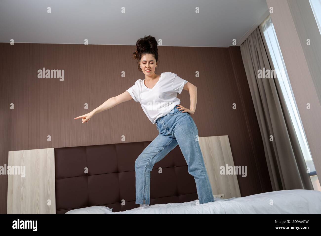 Positive expressions. Happy young woman dancing on the bed in the ...