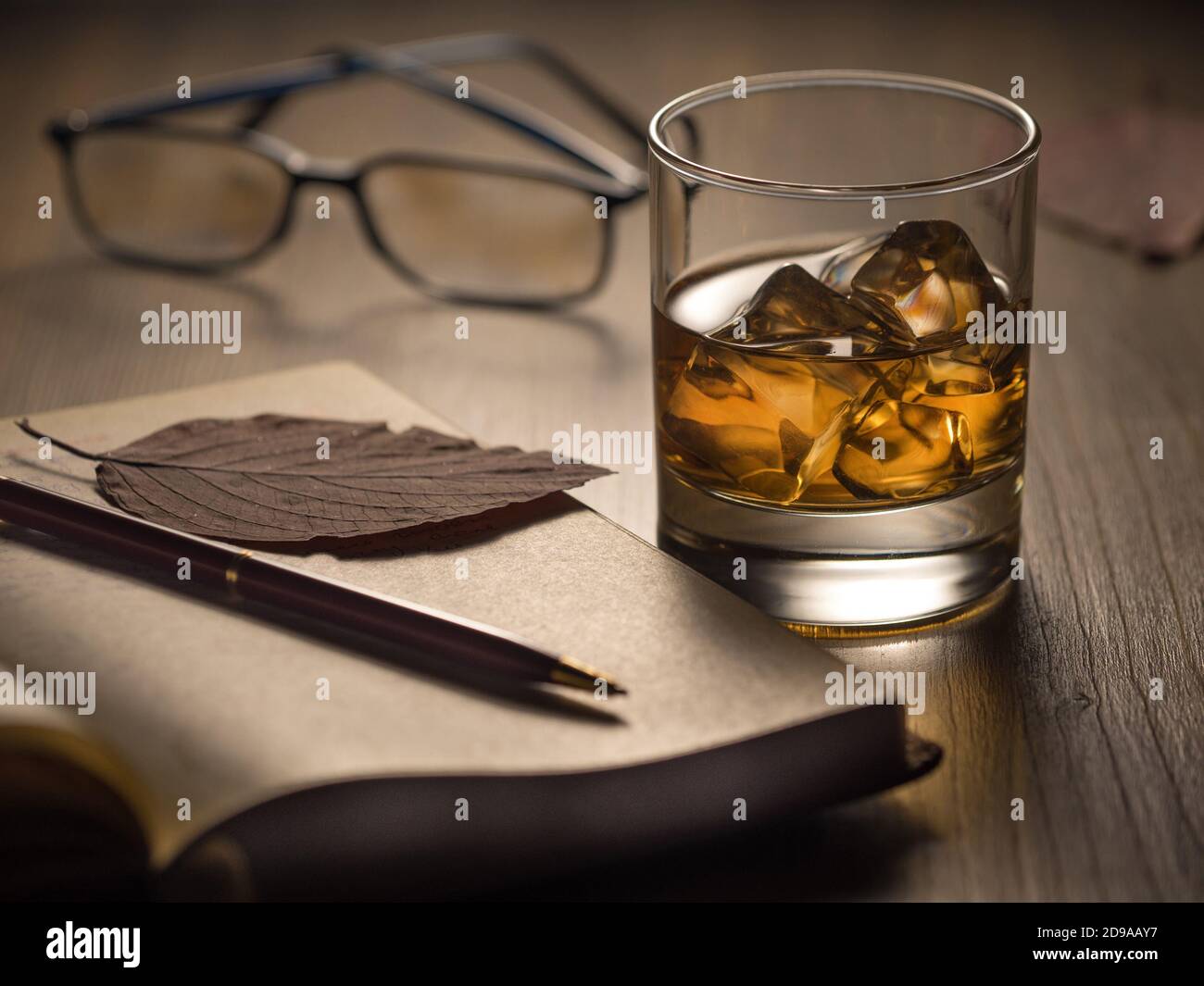 Backlit glass of whisky on the rocks on a wooden table, with notebook ...