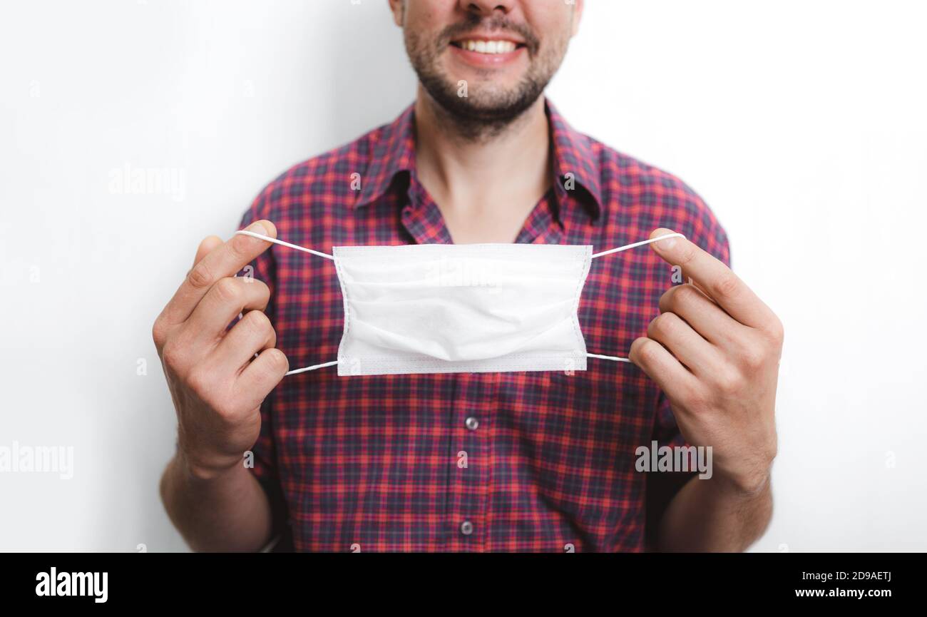 a man in a red checked shirt wears a medical mask against a white wall ...