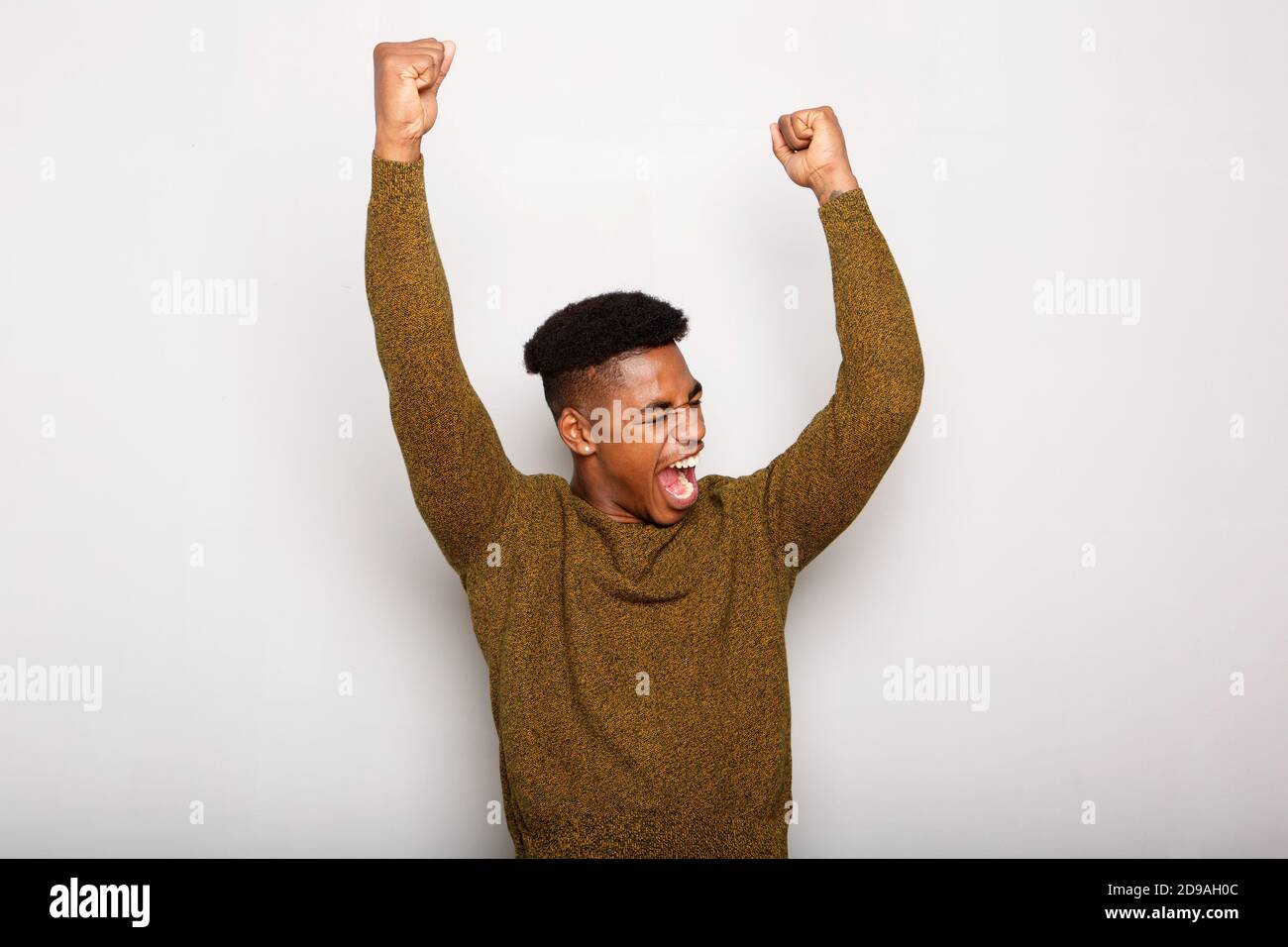 Portrait of happy young black man with arms raised in joy against gray ...