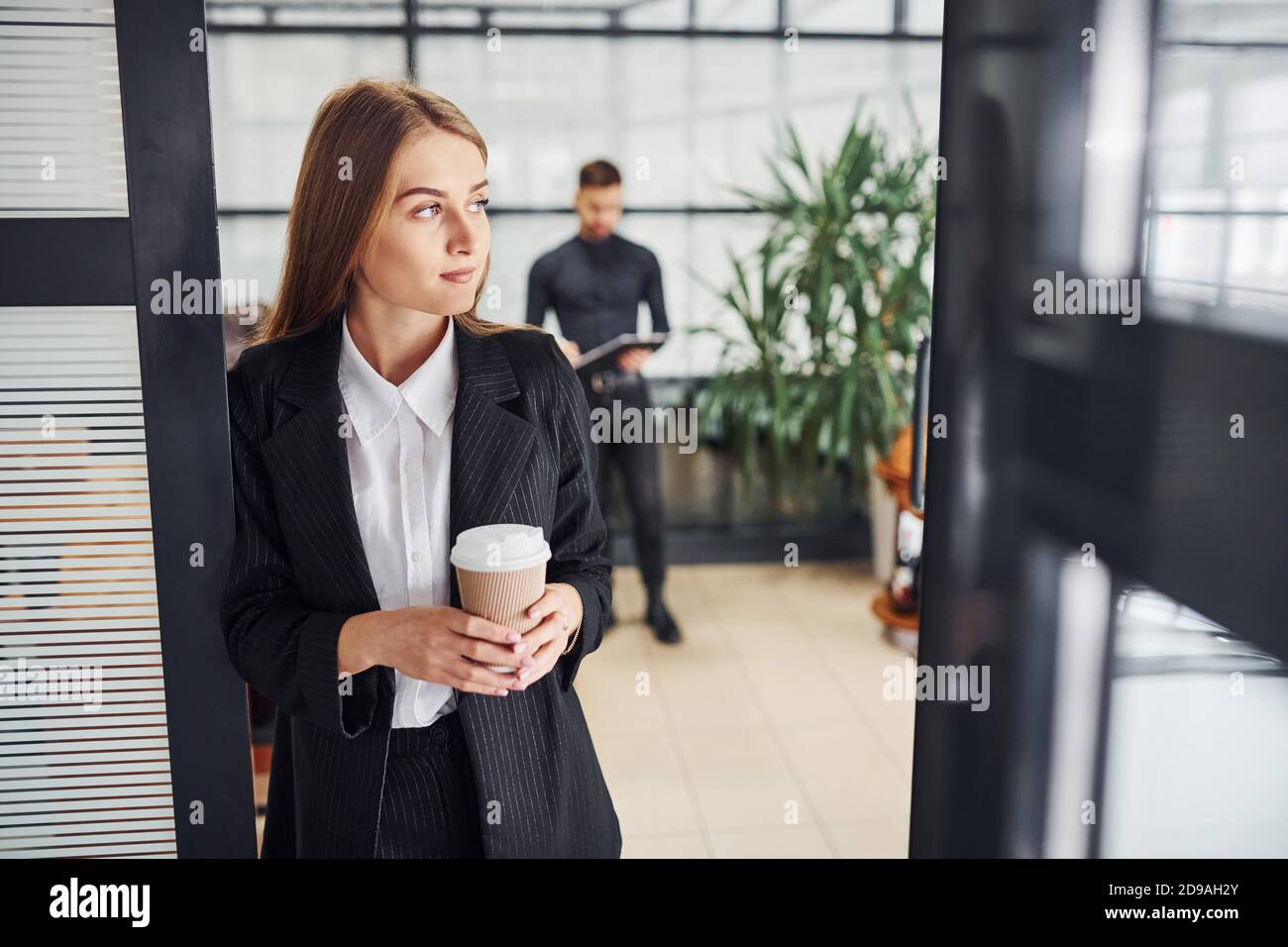 Modern businesswoman standing indoors in office. Her male colleague ...