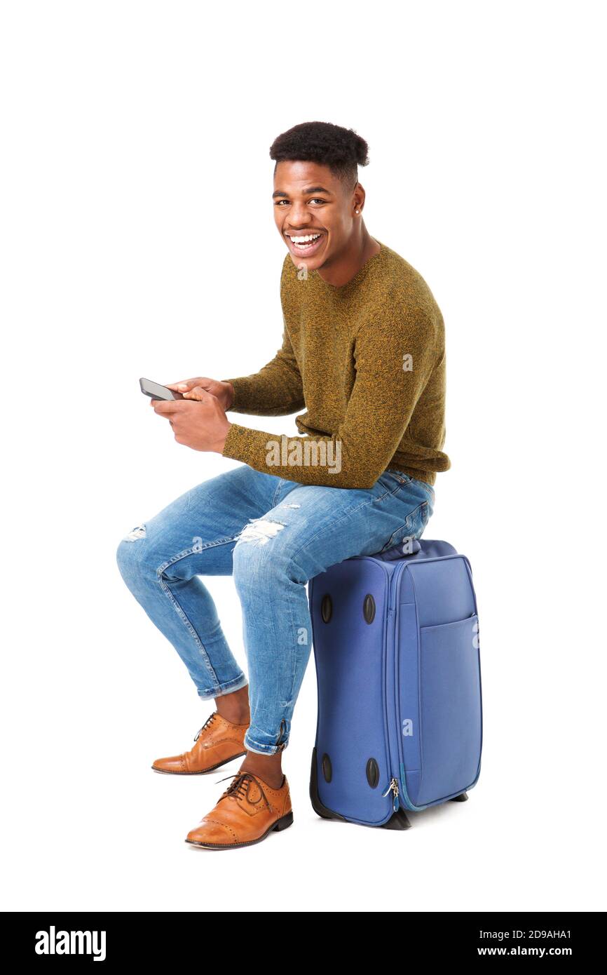 Portrait of happy travel man sitting with cellphone on suitcase against ...