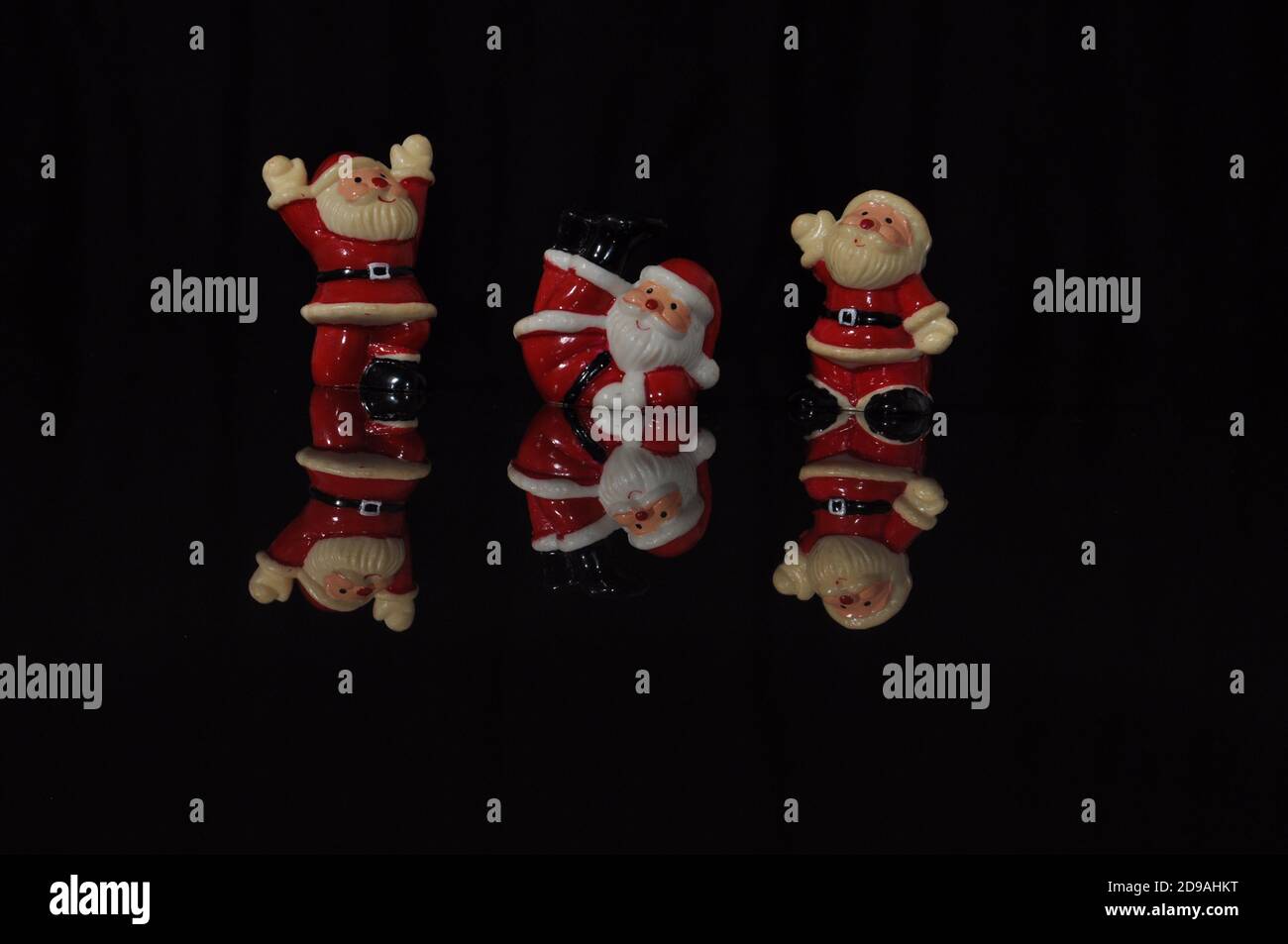 A christmas display of models of Father Christmas on a reflective black ...