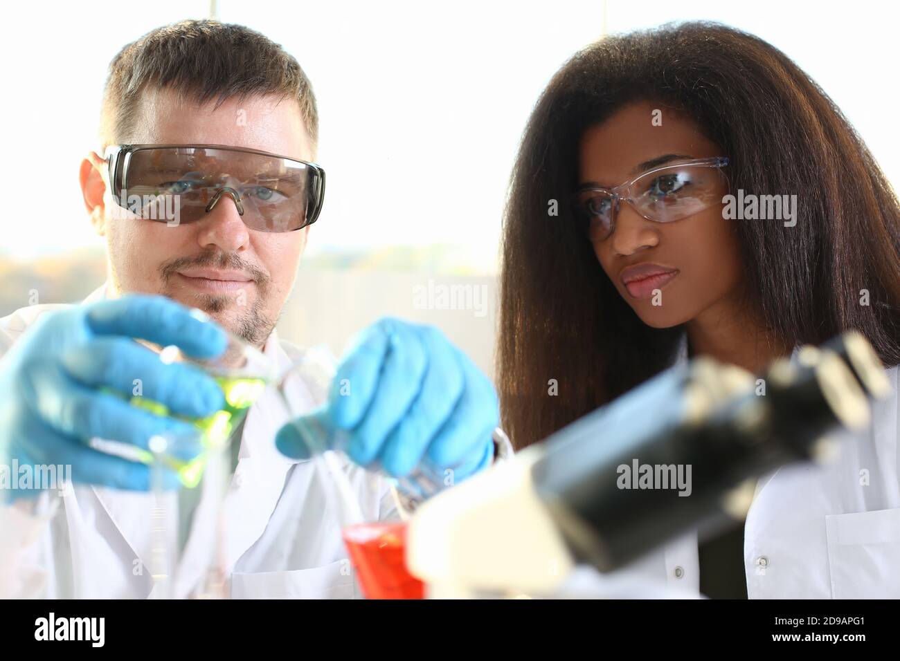 Scientists in glasses and gloves with test tubes and flasks in their ...