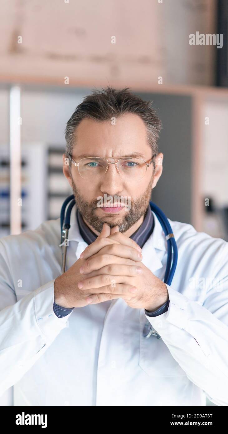 Vertical photo. A doctor with a stethoscope looks closely at the camera ...
