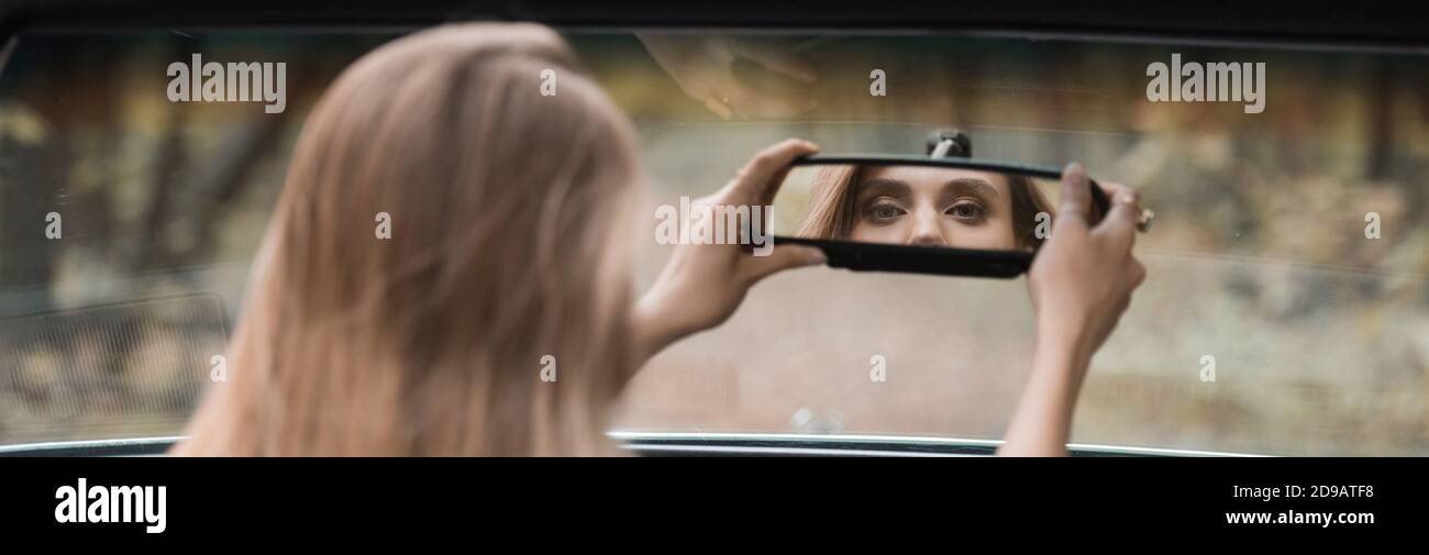 back view of young woman adjusting rearview mirror in car on blurred ...