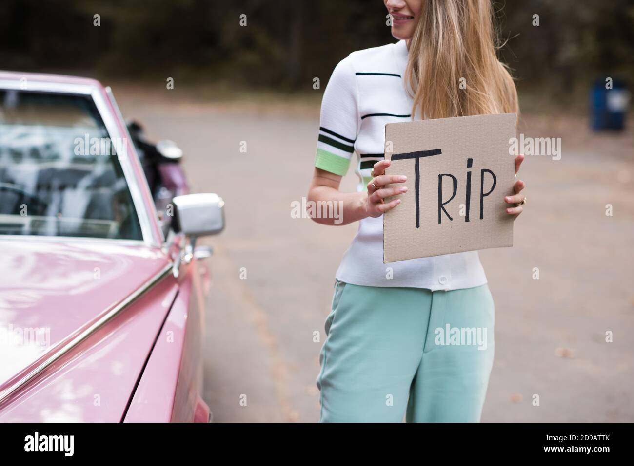 cropped view of woman holding card with trip lettering near cabriolet ...