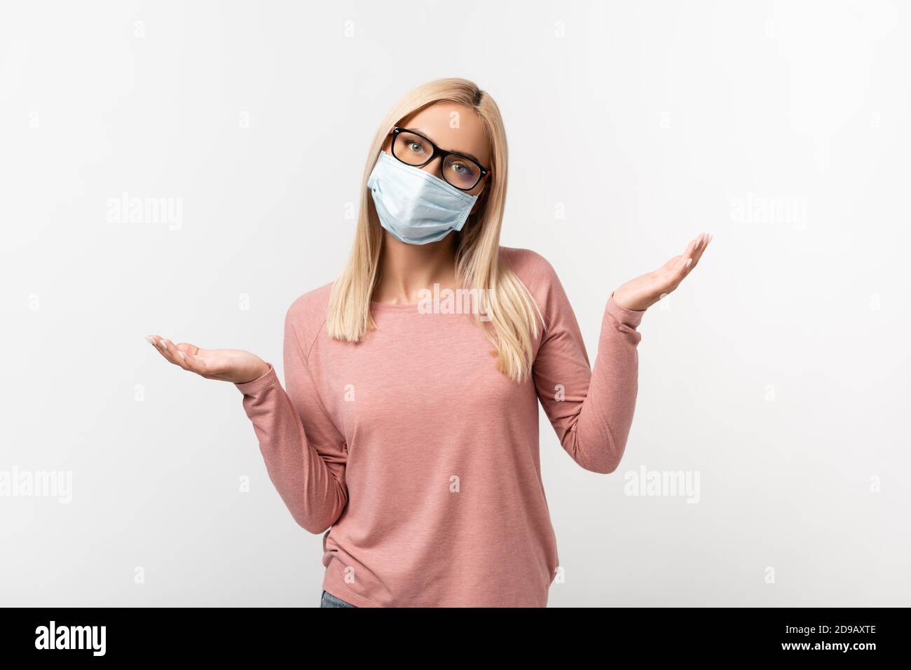 Blonde woman in medical mask and eyeglasses showing confused sign ...