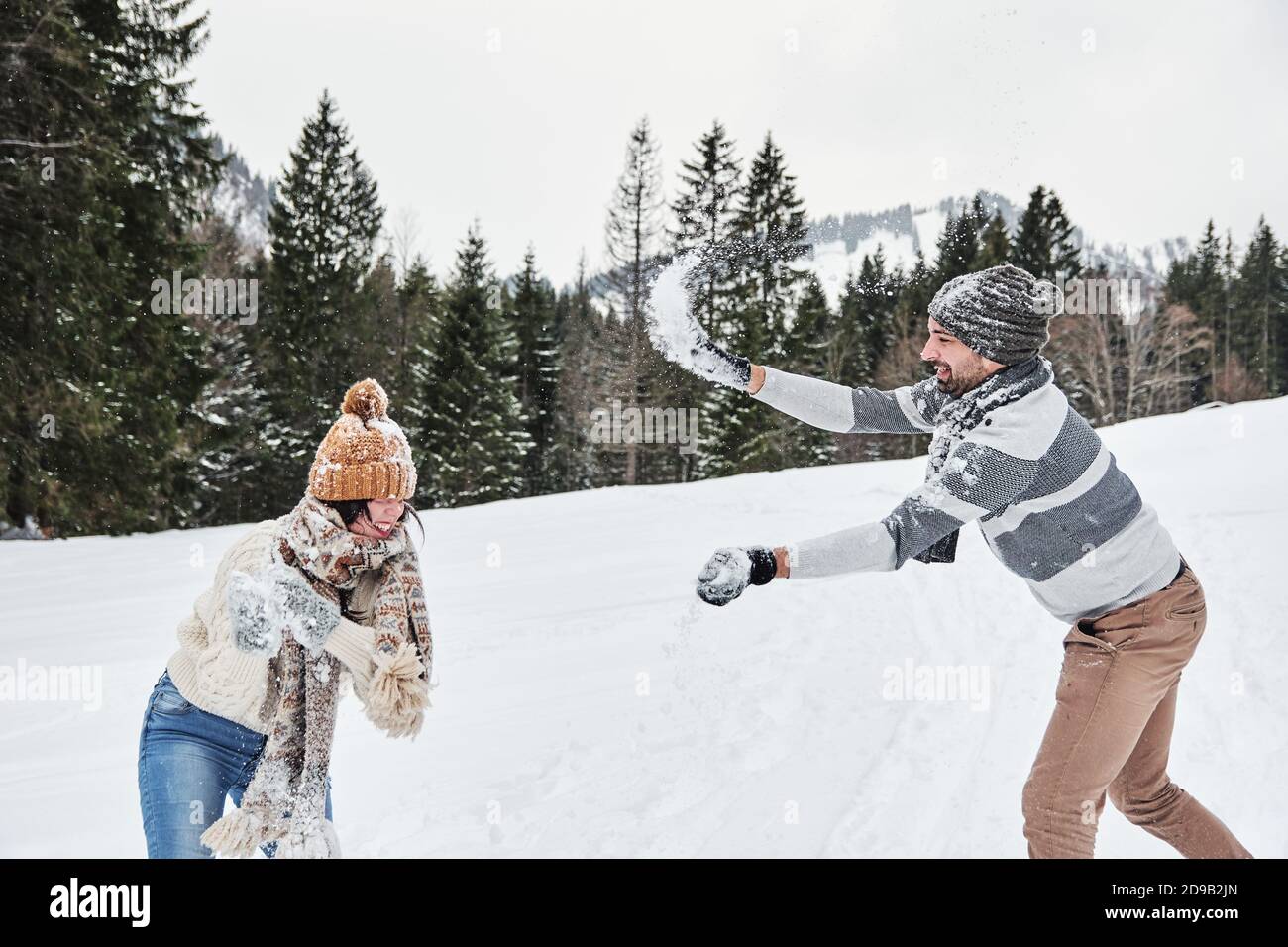 Cheerful young Caucasian couple having a snowball fight in the snow ...