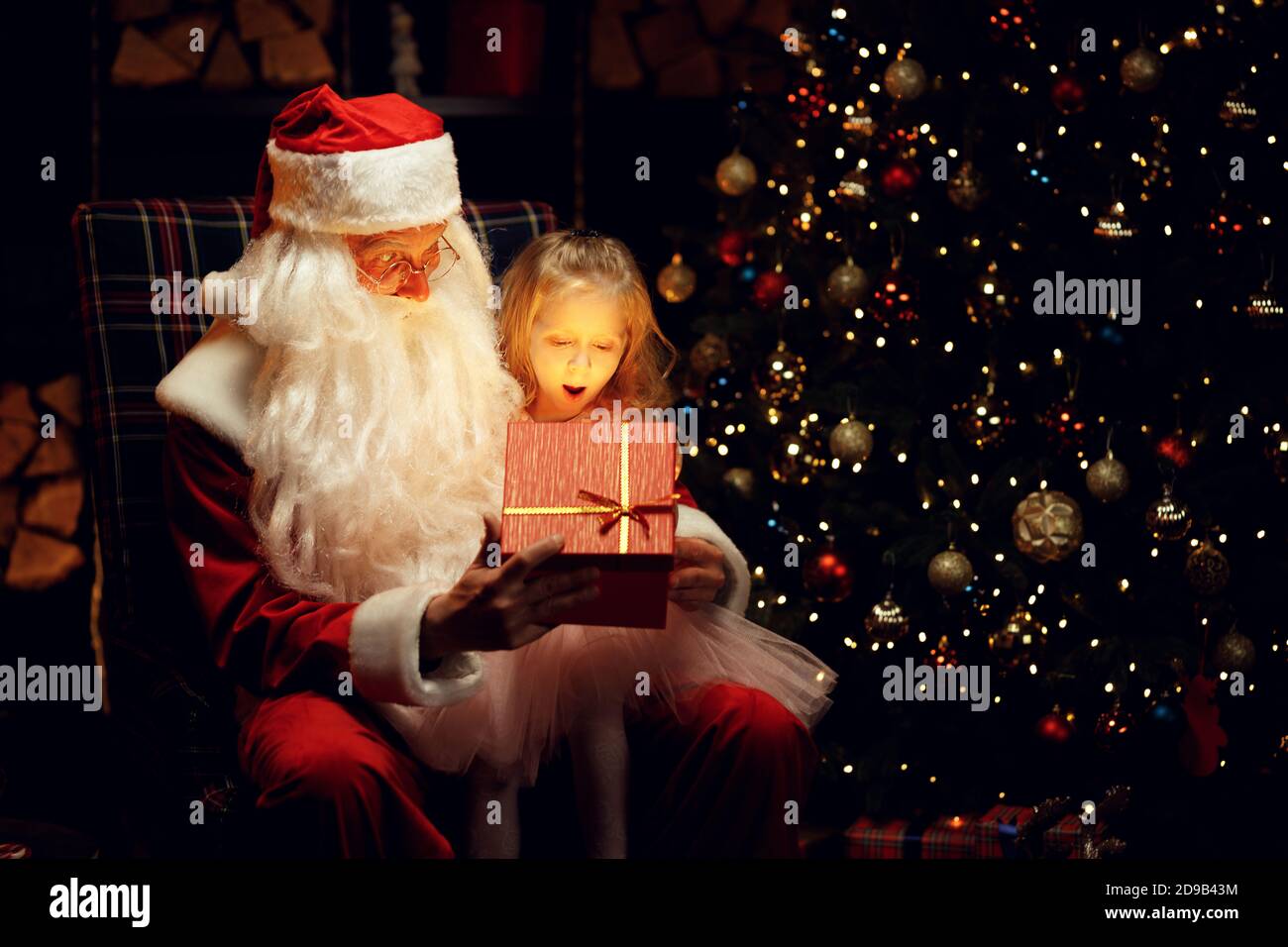 Santa Claus and little girl open a Christmas present Santa gives a ...
