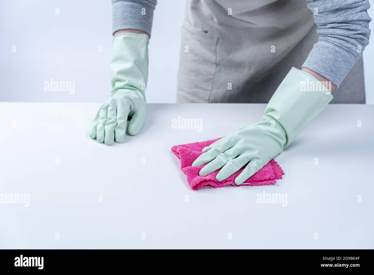 Young woman housekeeper in apron is cleaning, wiping down table surface ...