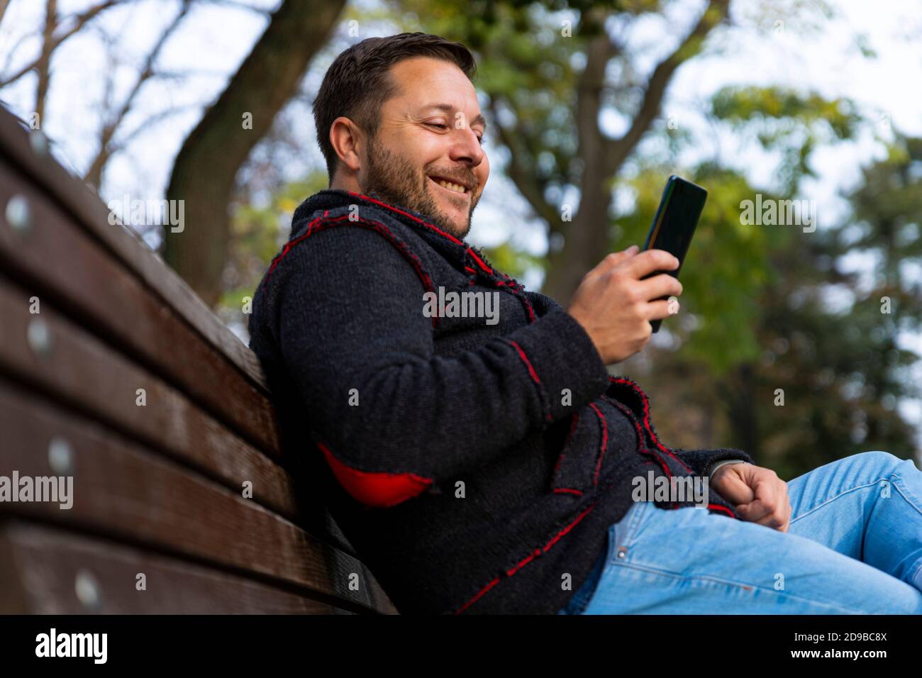 Man smiling and sitting on the bench in the park at autumn with ...