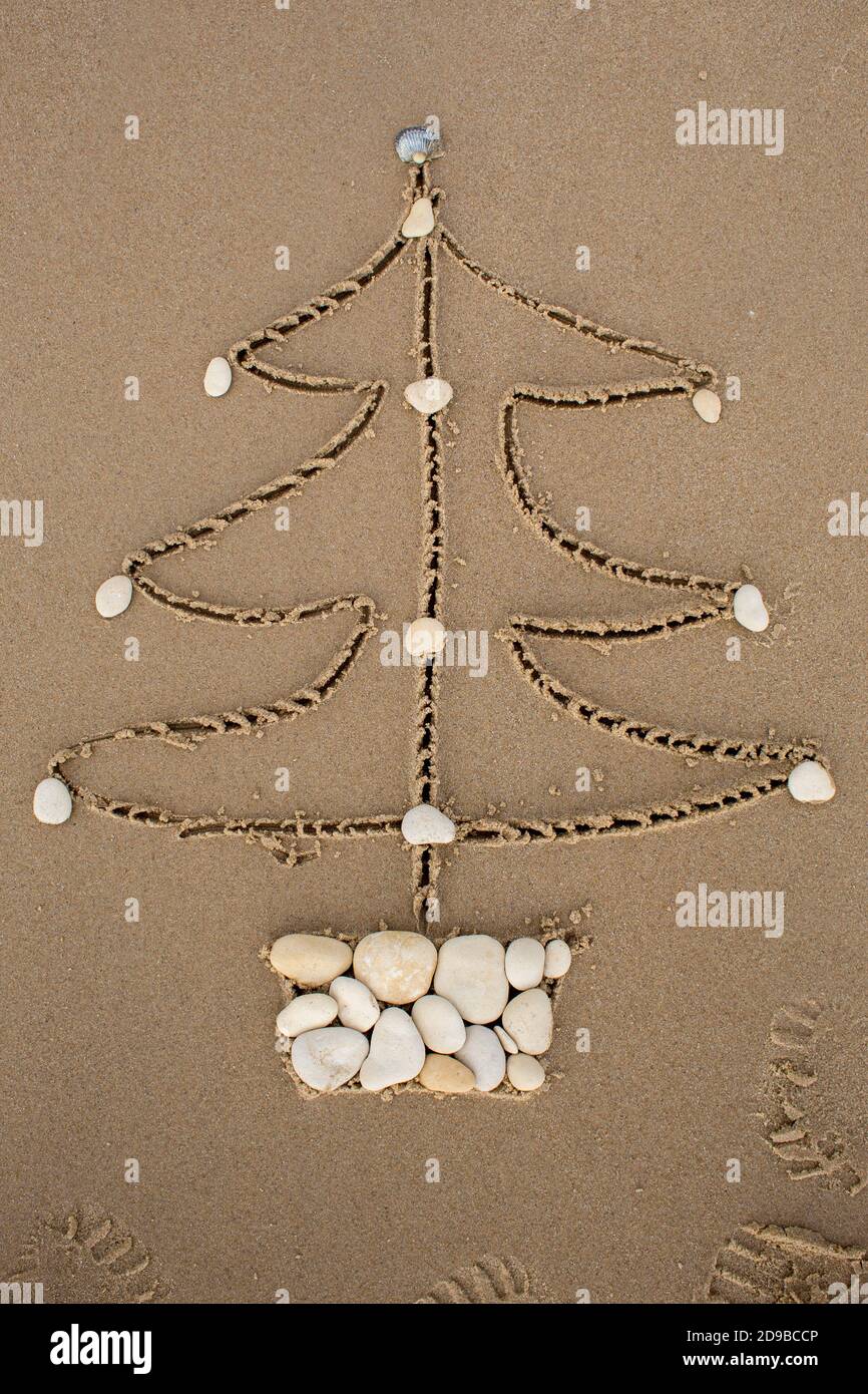 Christmas tree drawn in the wet sand and decorated with pebbles and sea ...