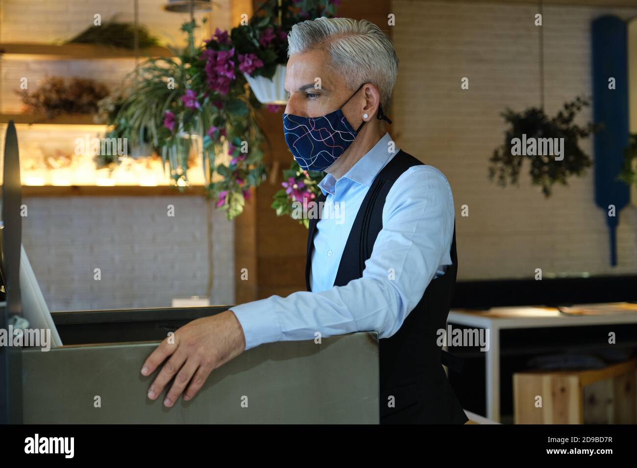 Waiter wearing face mask checking the tables on a counter touch screen ...