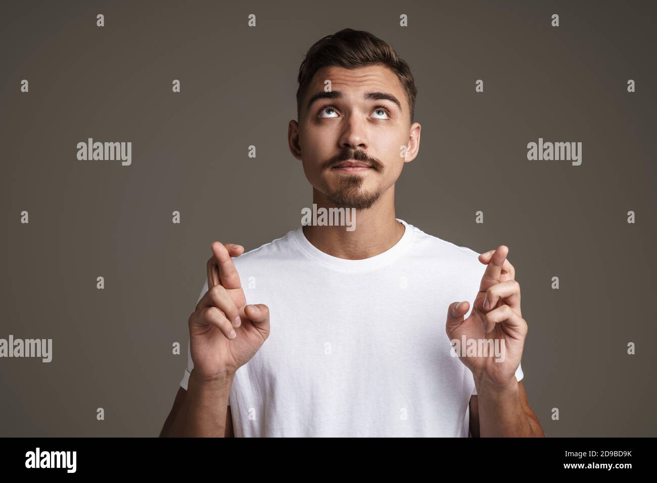 Image of thinking unshaven guy posing with fingers crossed for good ...