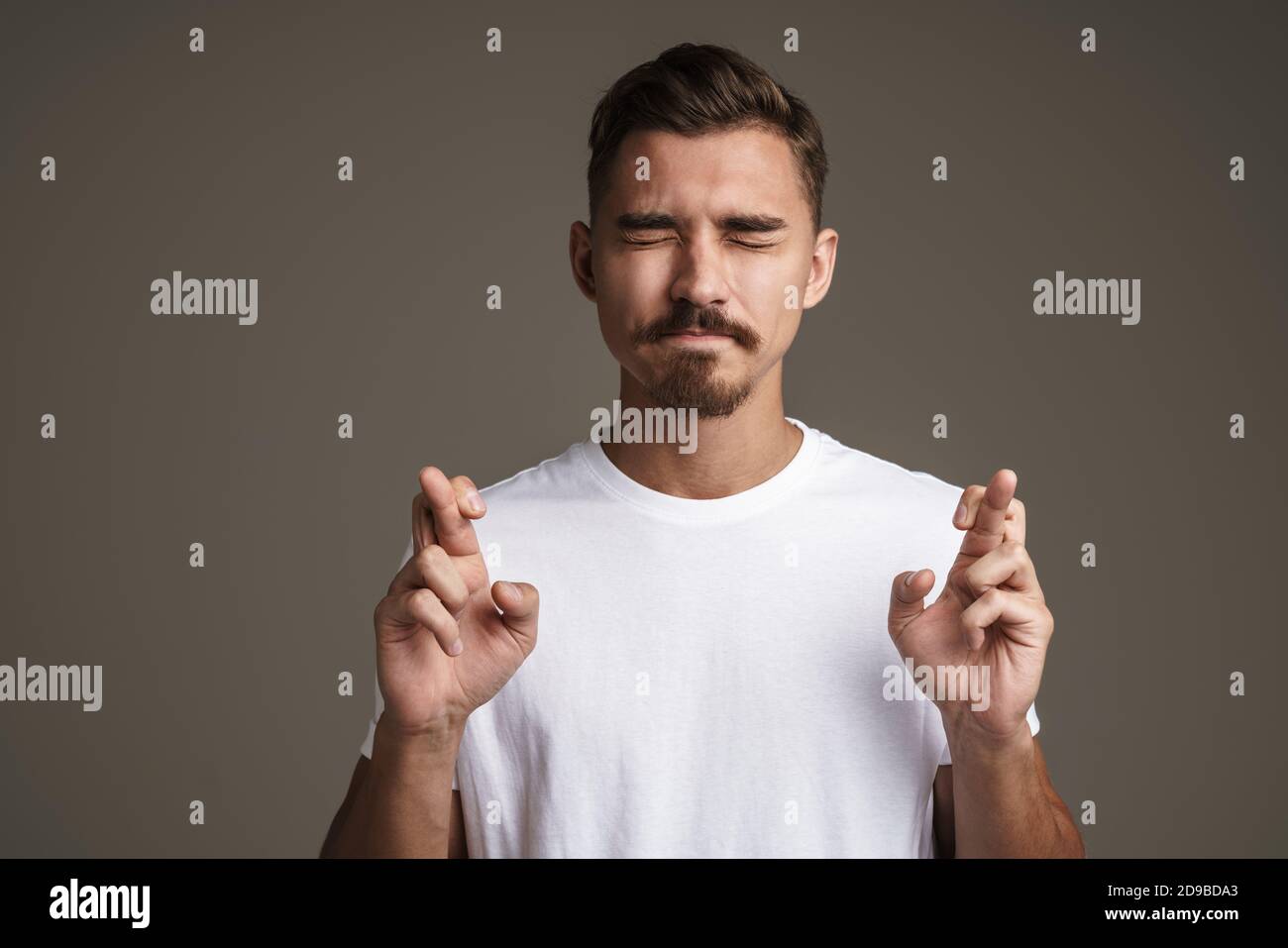 Image of tense unshaven guy posing with fingers crossed for good luck ...