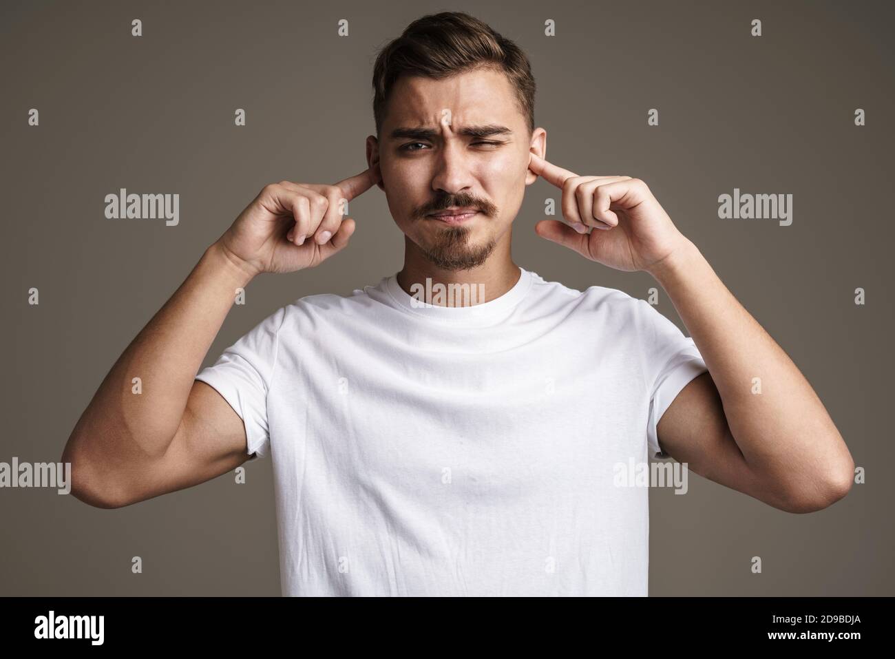 Image of caucasian displeased guy plugging his ears isolated over grey ...