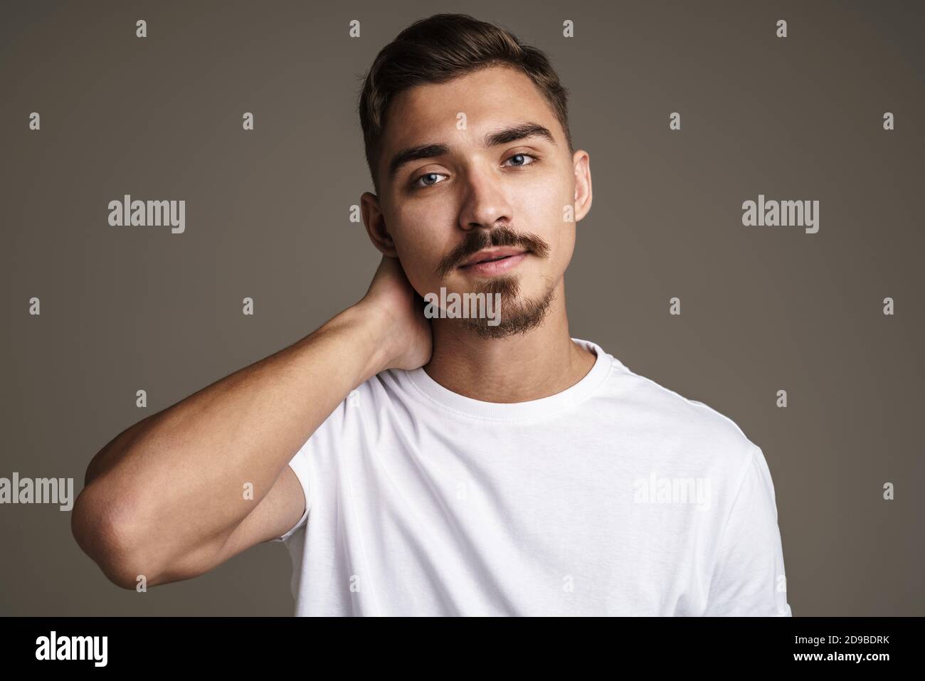 Image of caucasian handsome guy rubbing his neck while posing on camera ...
