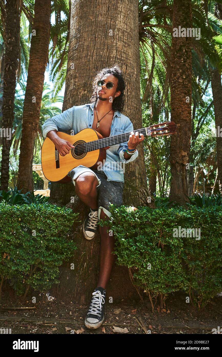 Young musician with classical guitar playing under the shade of some ...