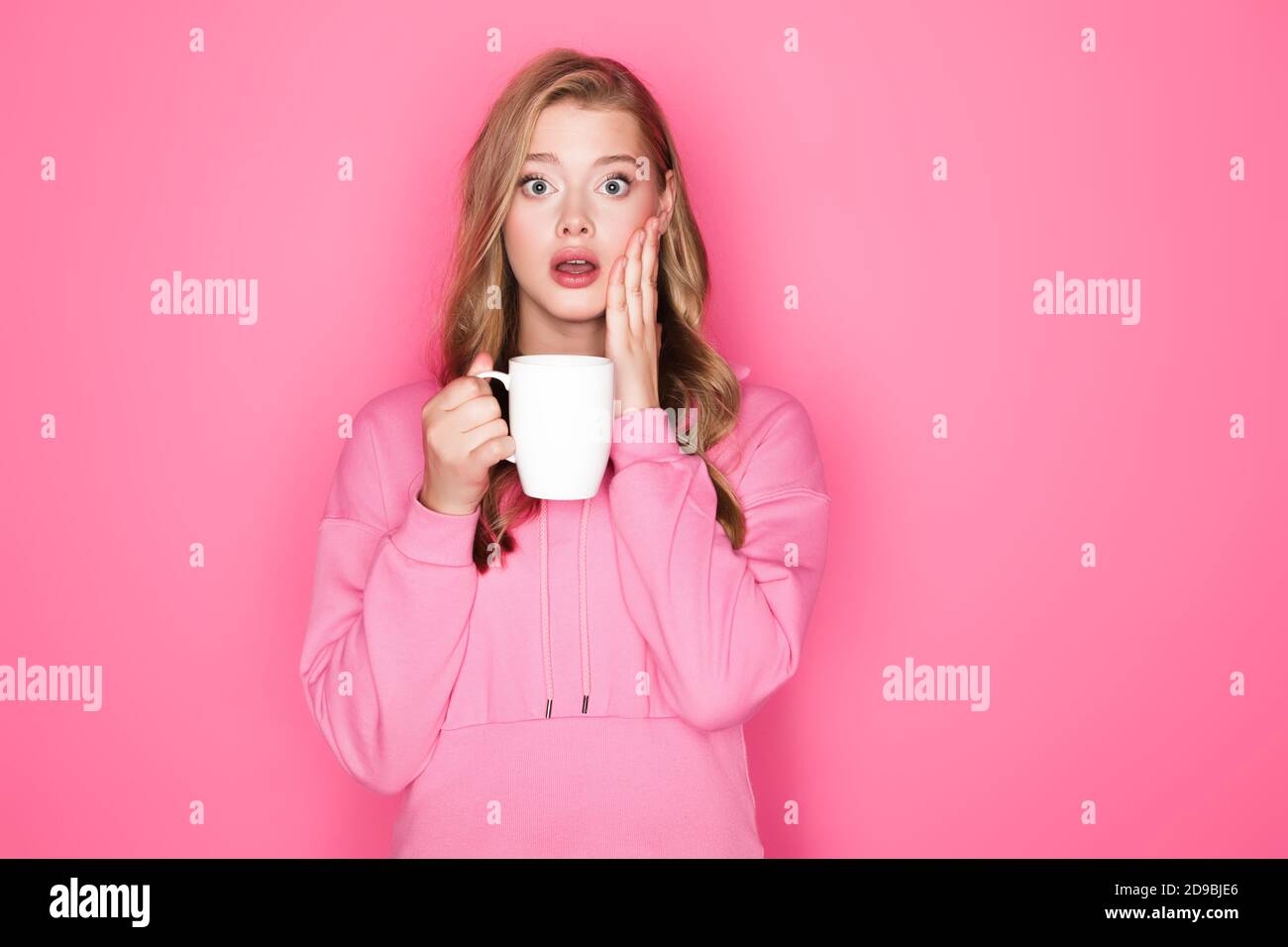shocked beautiful woman with open mouth and mug on pink background ...