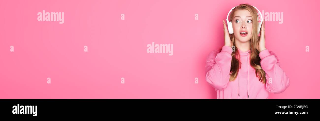 shocked beautiful woman listening music in headphones on pink ...