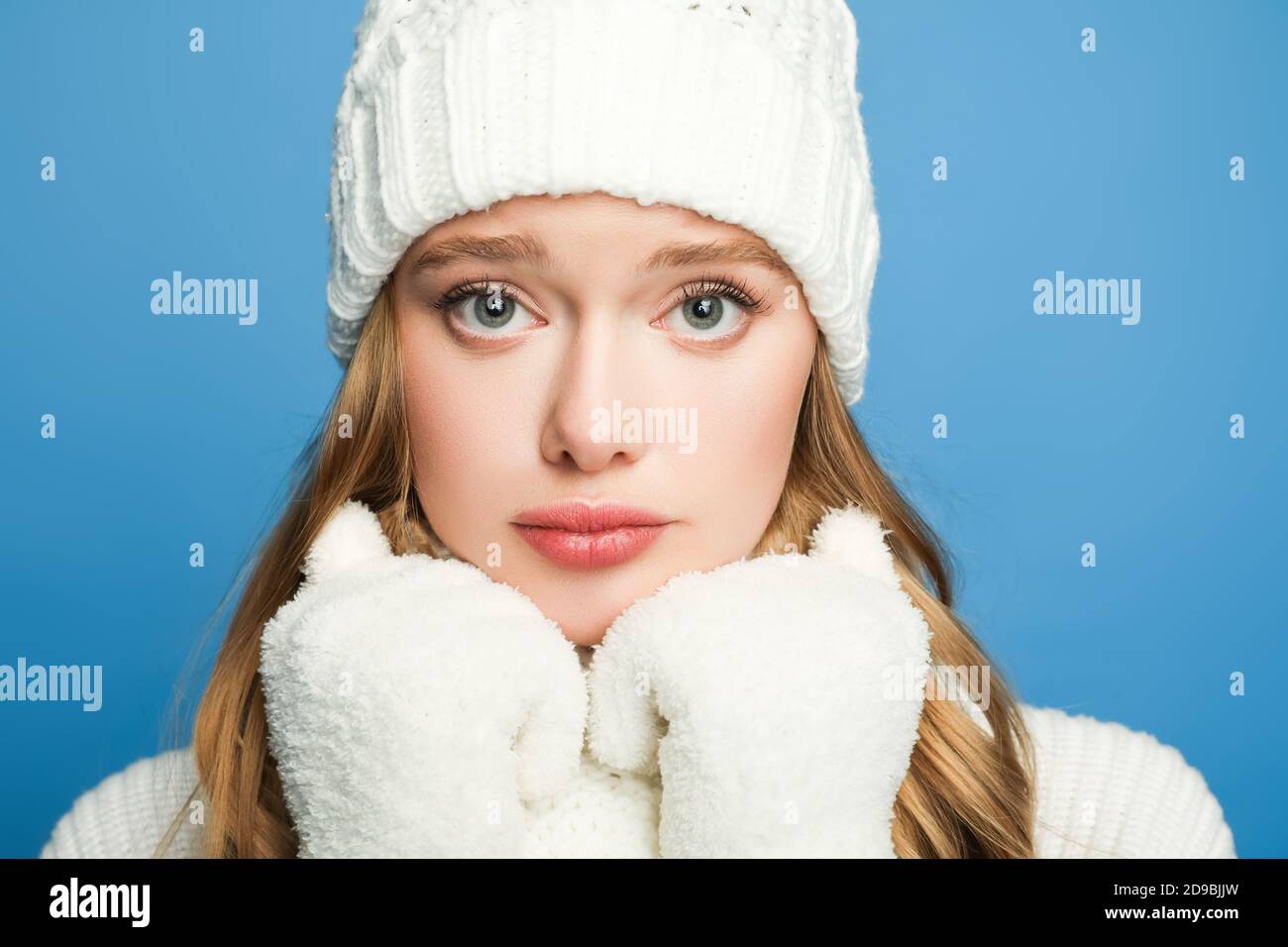 portrait of sad beautiful woman in winter white outfit isolated on blue ...