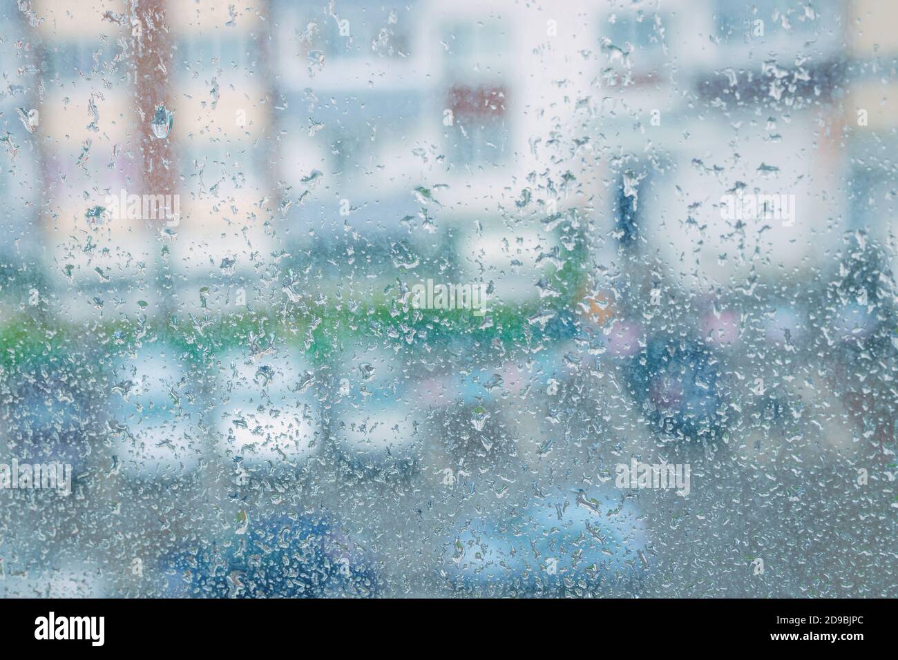 View through a rainy window on a blurred house and car parking. Bad ...