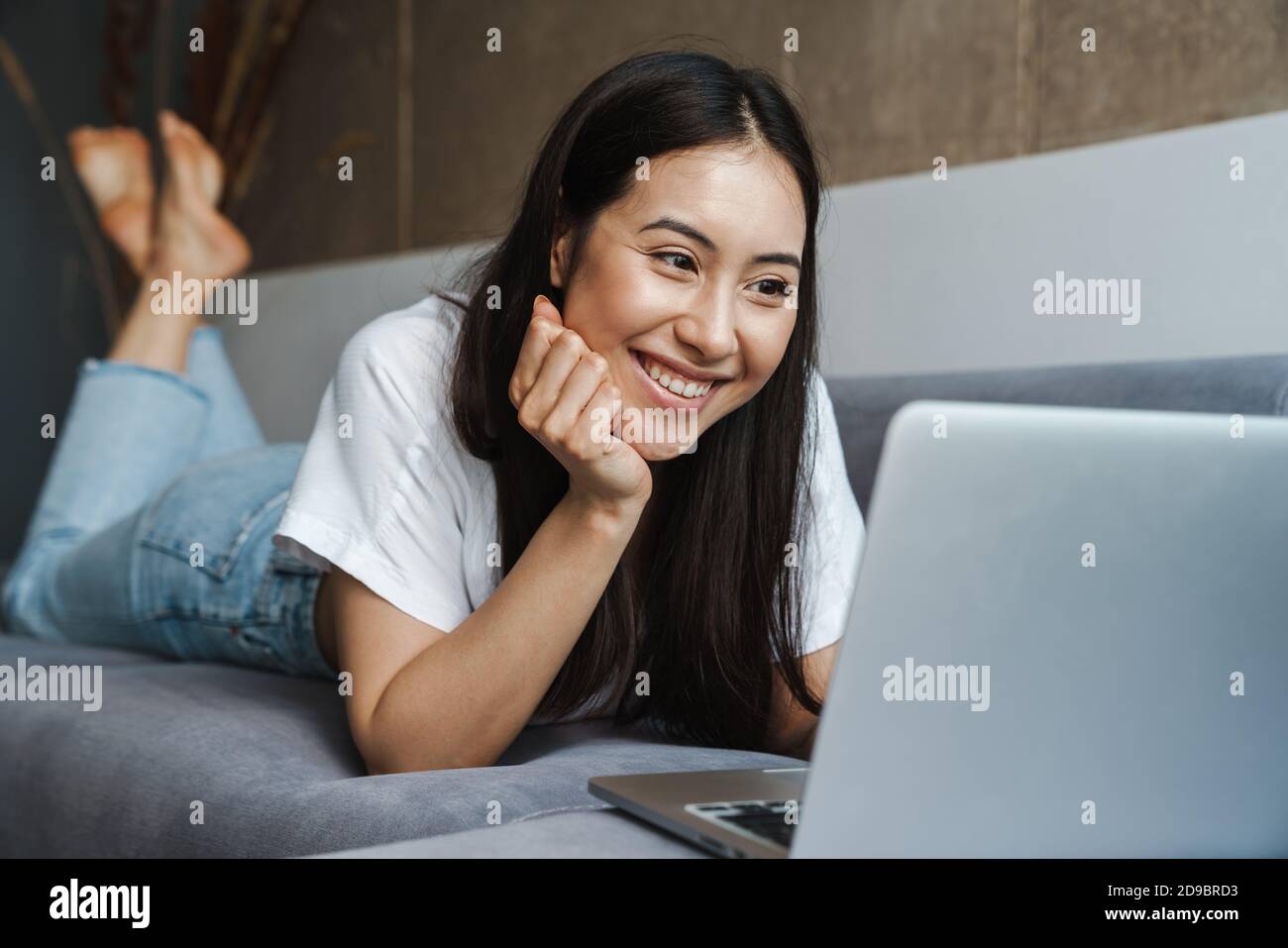 Happy young woman on a video call through laptop computer while laying ...