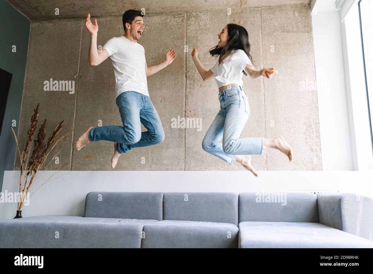 Cheerful young couple jumping on couch at home Stock Photo - Alamy