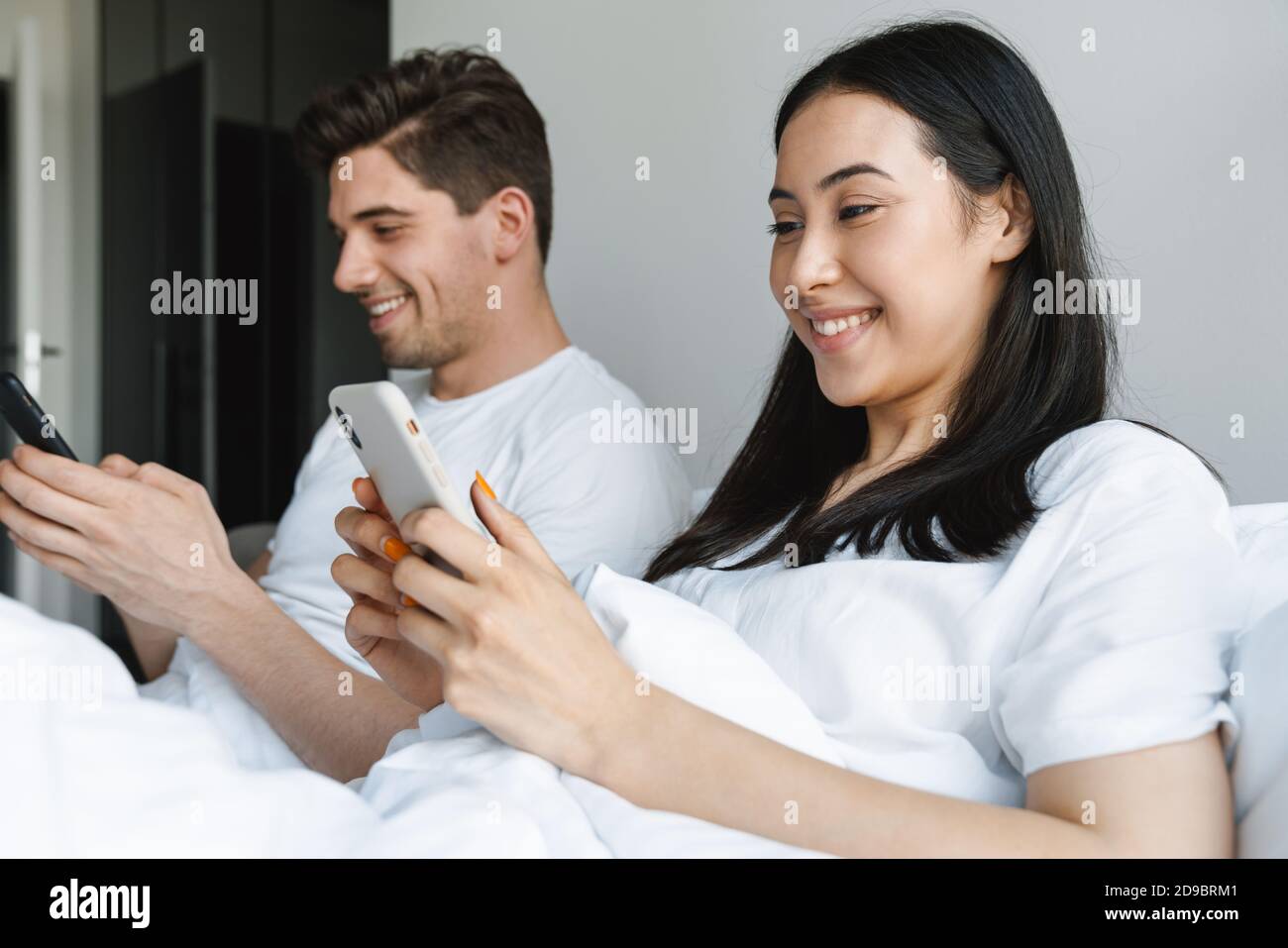 Photo of a positive young loving couple at home in bedroom lying in a ...