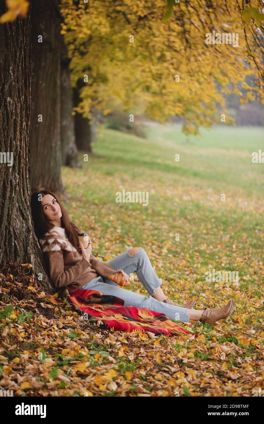 Beautiful woman in sweater, jeans and boots sitting under the maple ...