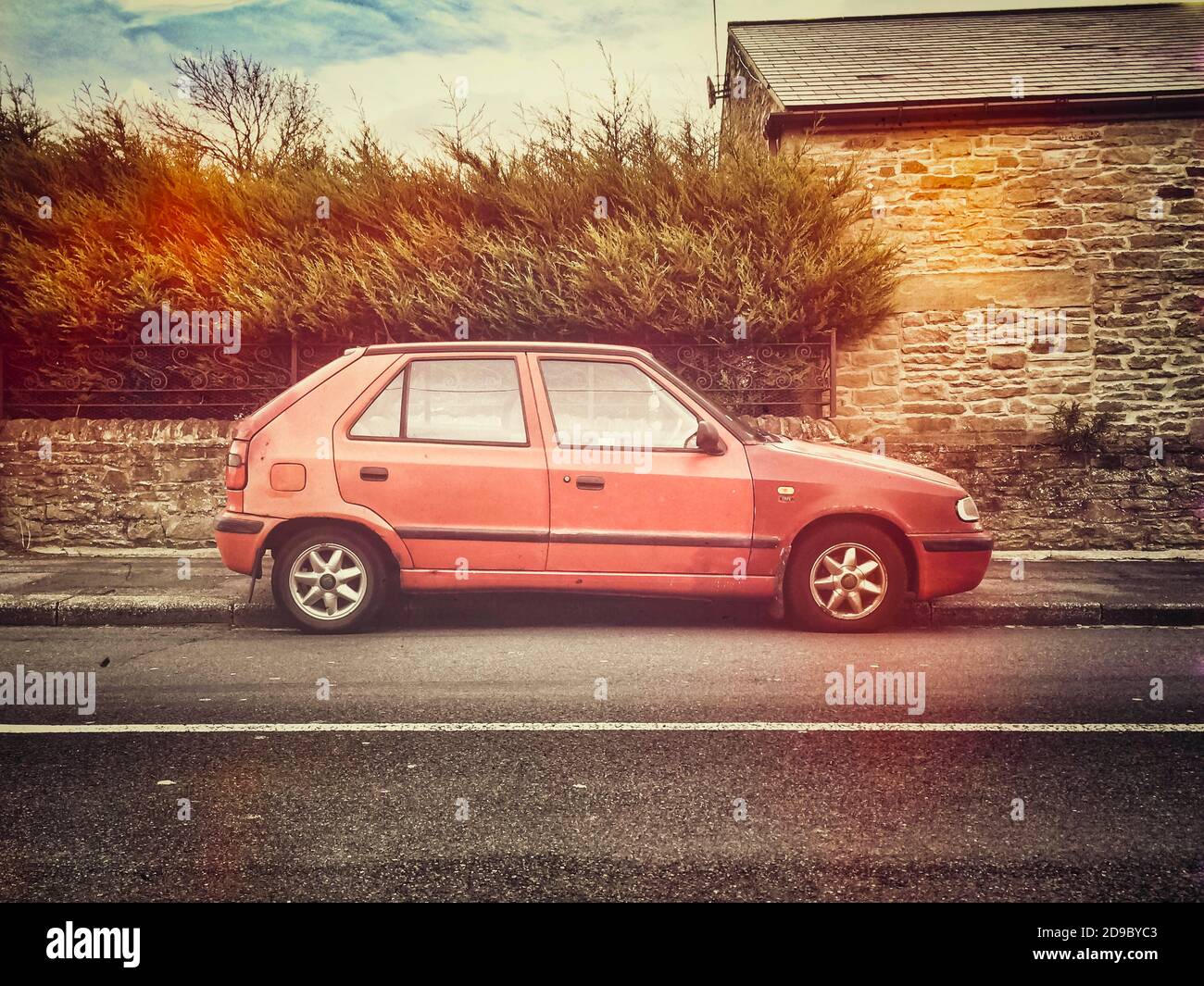 Old and faded red hatchback car with new front wing at the side of the ...