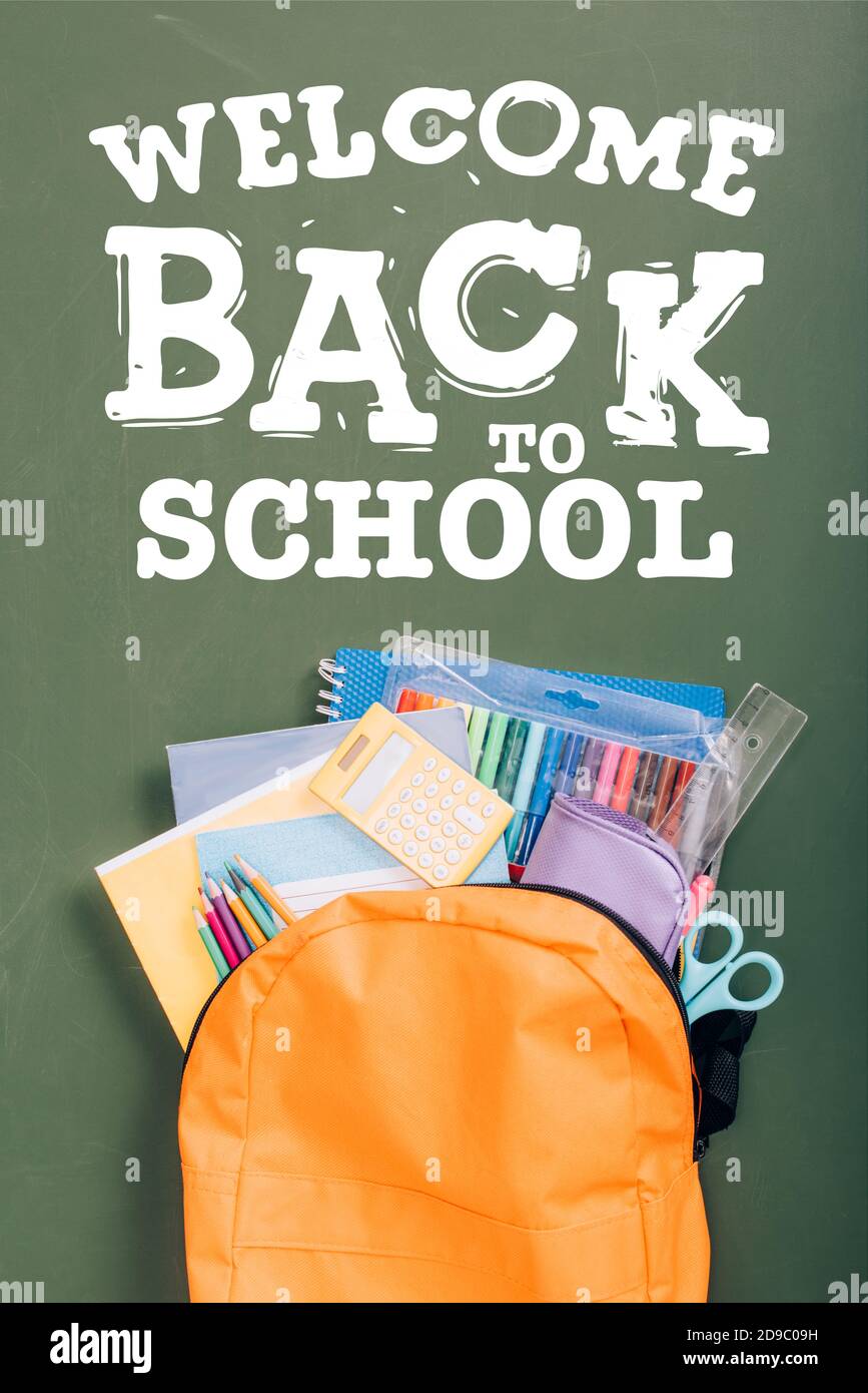 top view of backpack packed with school stationery on green chalkboard ...