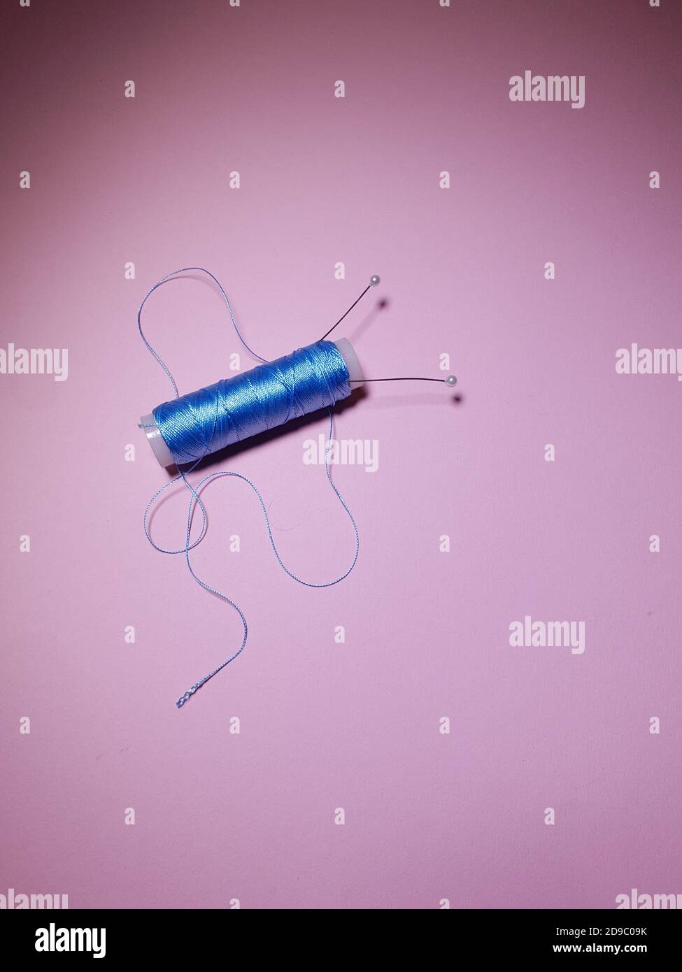 blue thread with needles on a pink background in the form of a ...