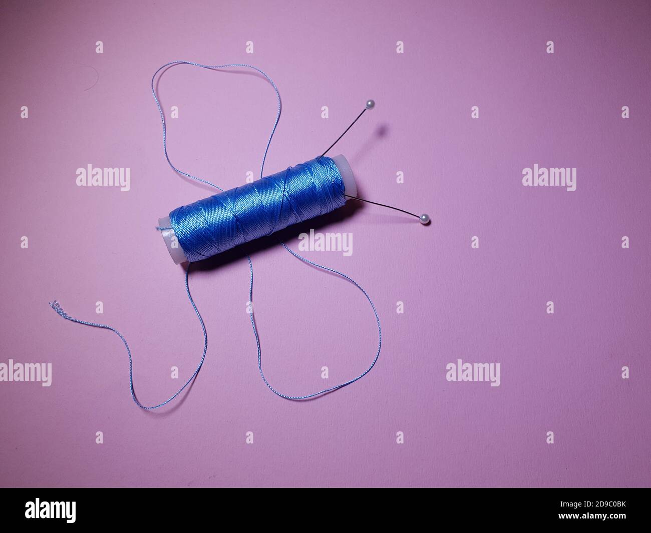 blue thread with needles on a pink background in the form of a ...