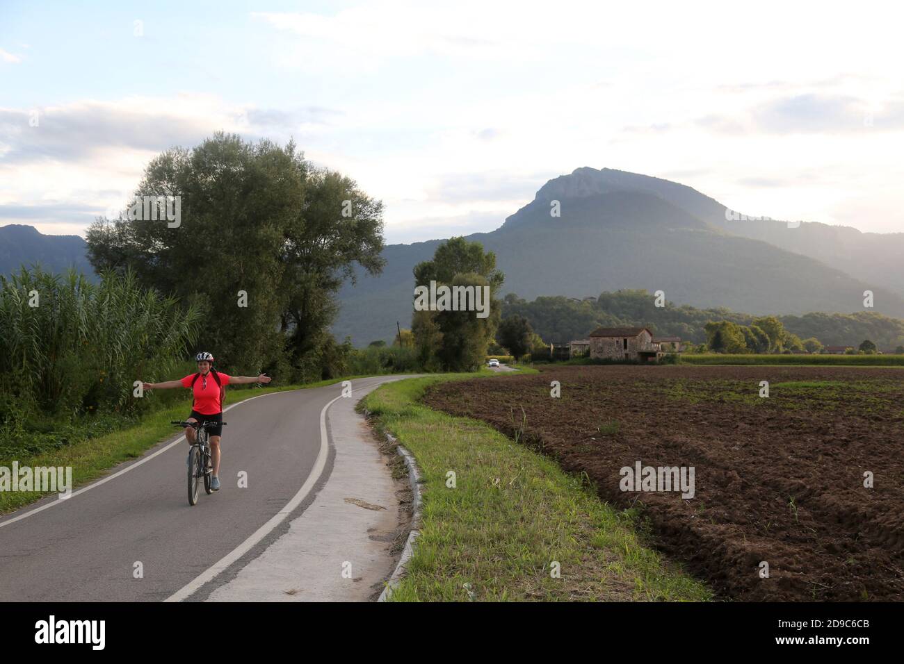 Woman biking in countryside in a narrow road with mountain background ...