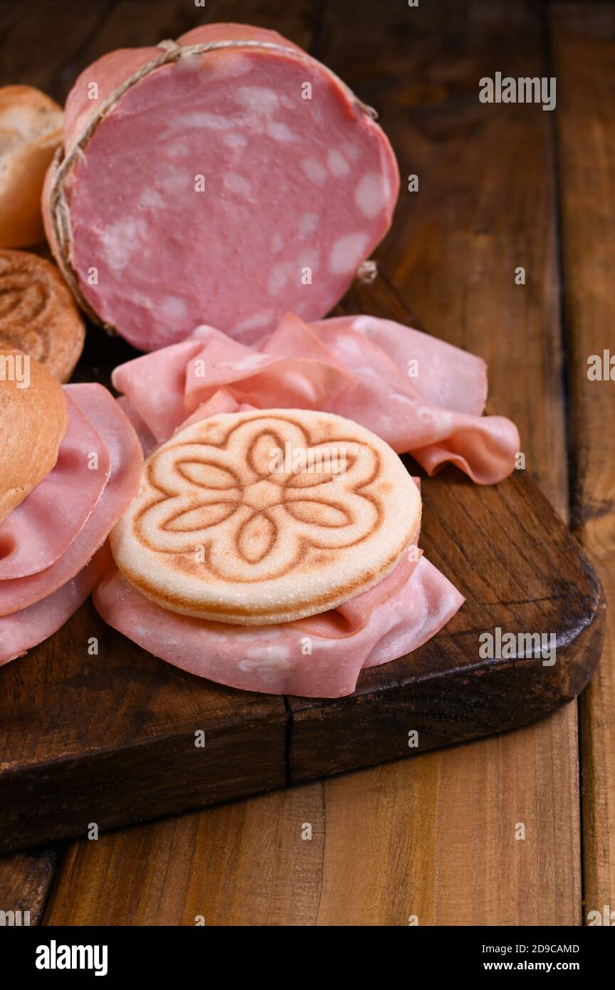 Big Mortadella and Tigelle on a wooden table. Assorted breads of ...
