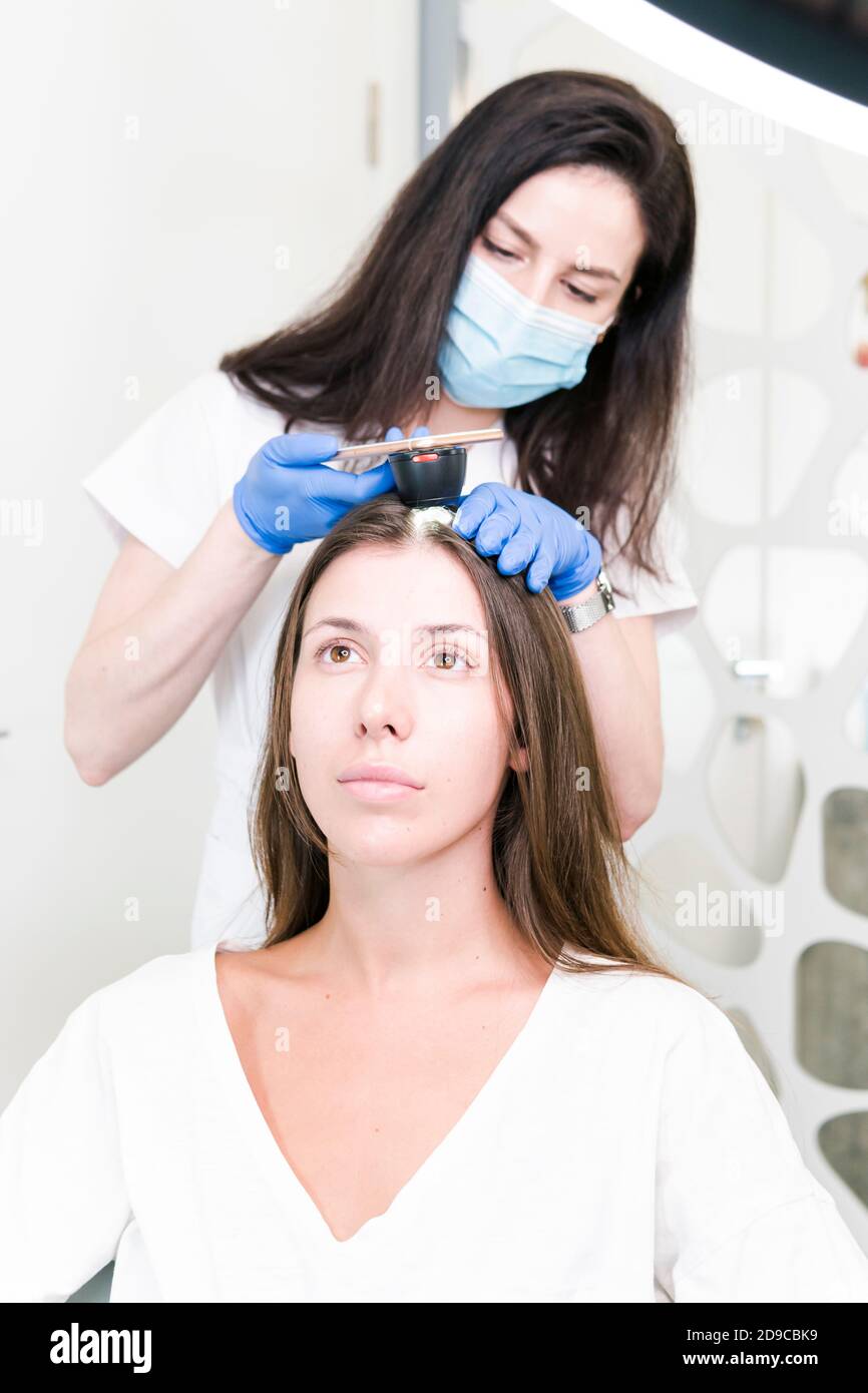 The doctor dermatologist examining client hair with a special apparatus ...